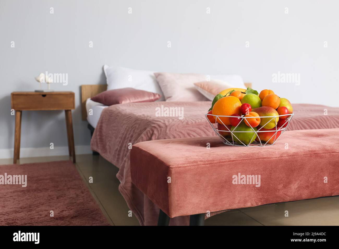 Basket with different fruits on bench near bed in bedroom Stock Photo ...