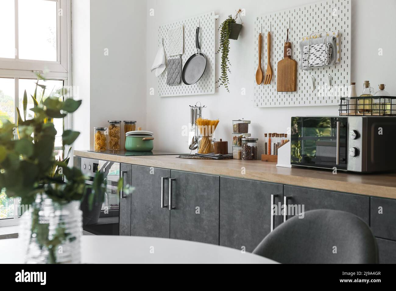 Stylish counters with utensils and pegboards on light wall in kitchen ...