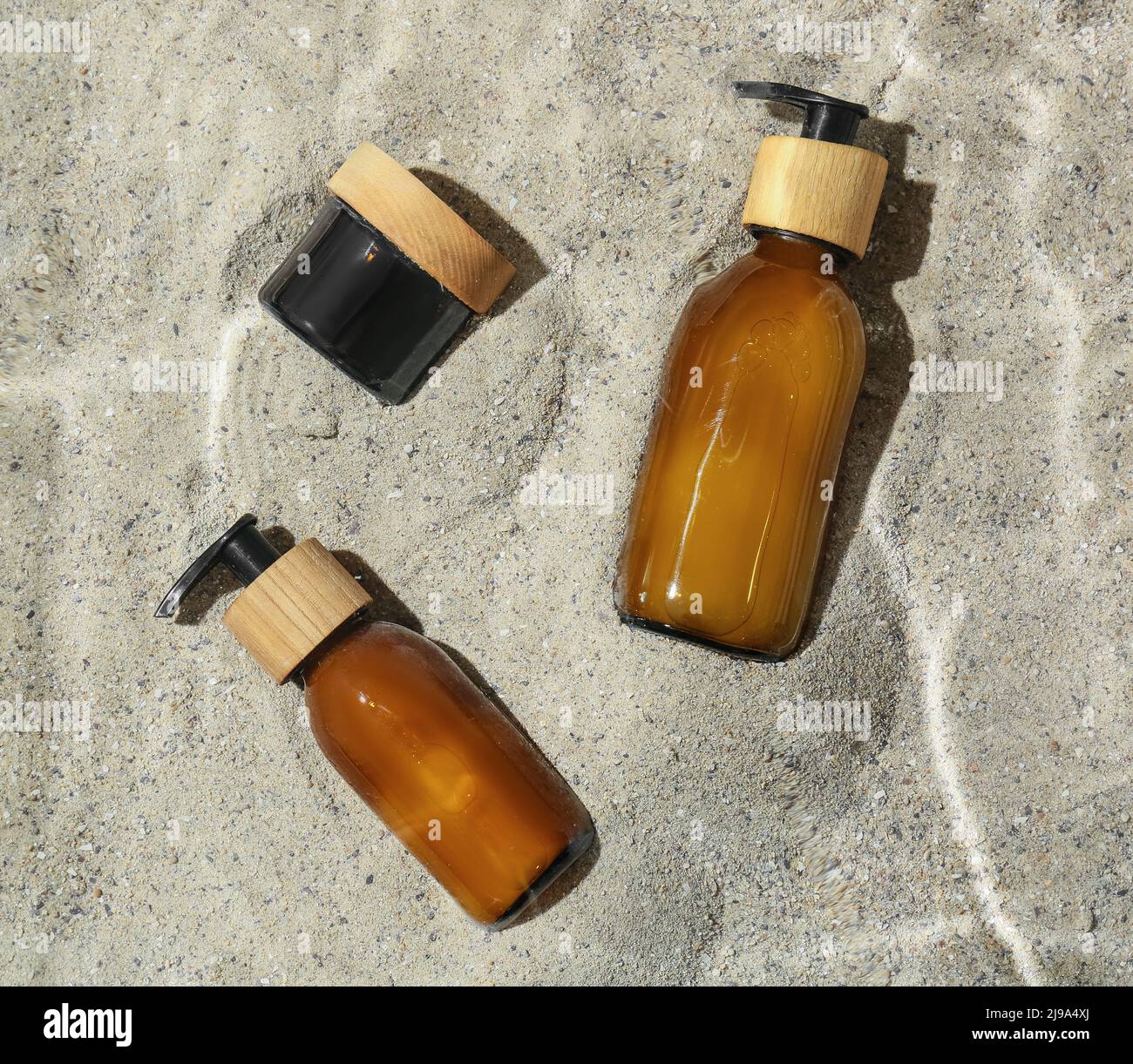 Dispenser bottles and jar of cosmetic product in water on sand ...