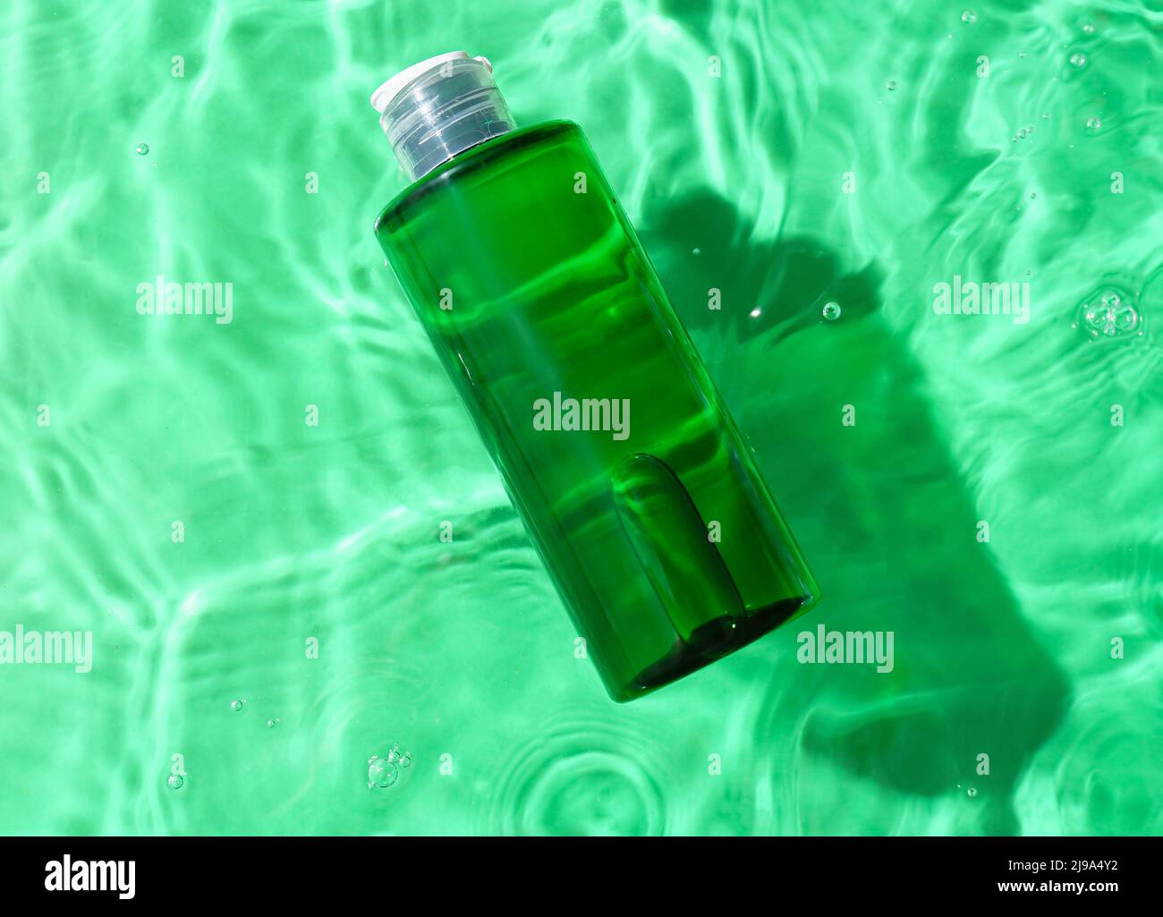 Bottle of cosmetic product in water on green background Stock Photo - Alamy
