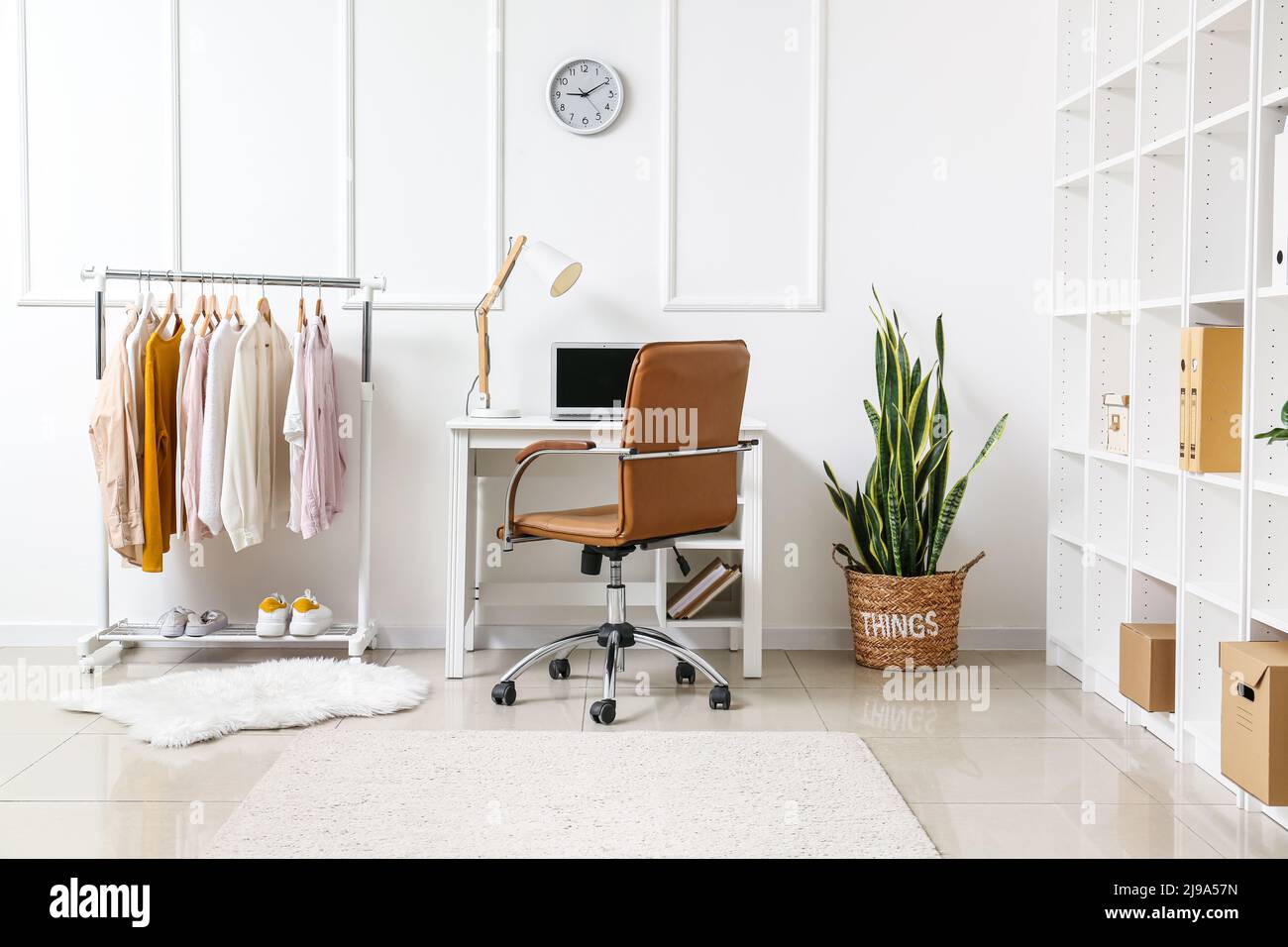 Interior of light room with modern workplace and rack with clothes ...