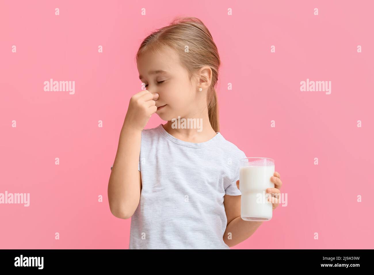 Cute little girl holding glass of milk and closing nose on color ...