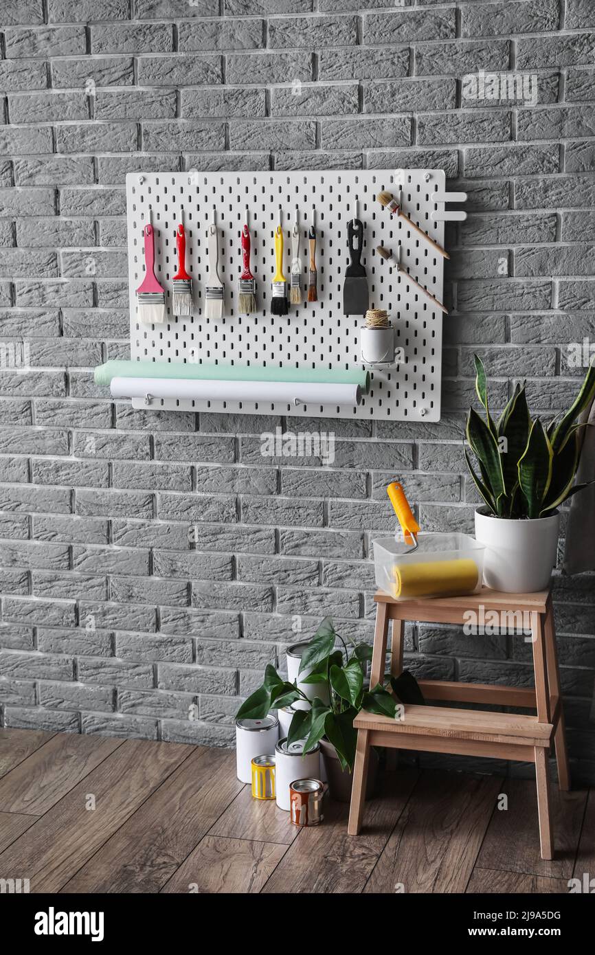 Stepladder stool with houseplant and pegboard with decorator's tools on grey brick wall in room ...