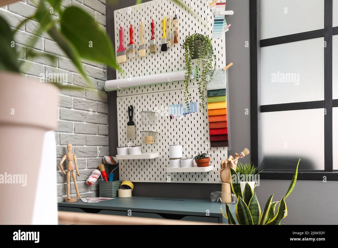 Pegboard with decorator's tools and houseplants in stylish workshop ...