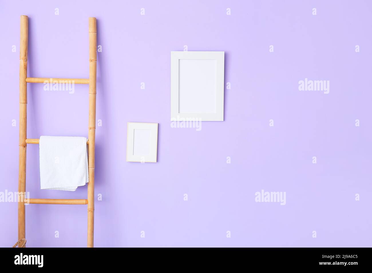 Ladder with towel and blank photo frames on lilac wall Stock Photo - Alamy