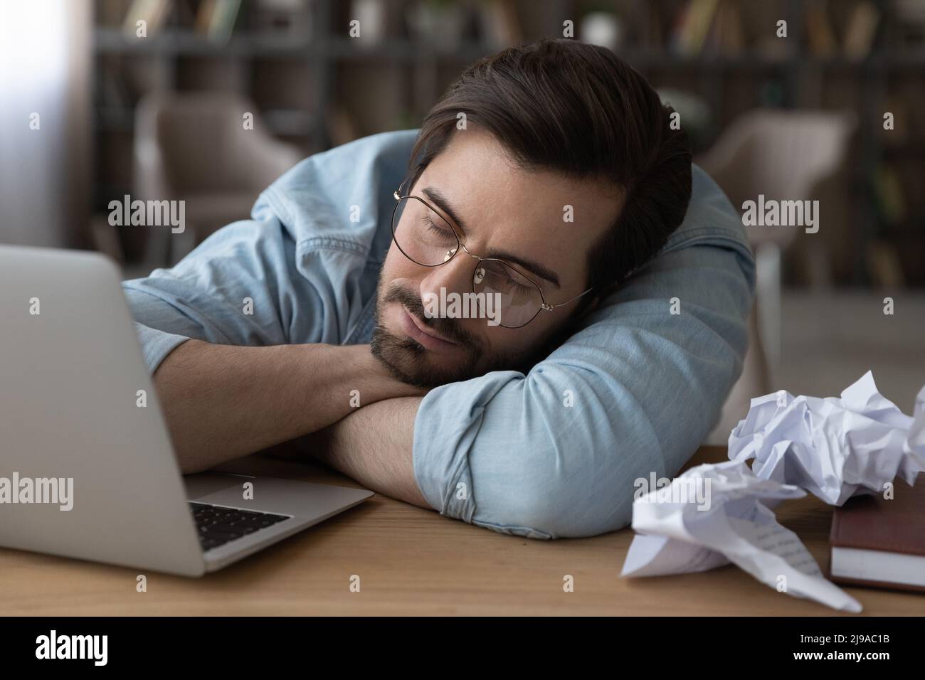 Tired male writer lie on desk sleep among crumpled papers Stock Photo ...