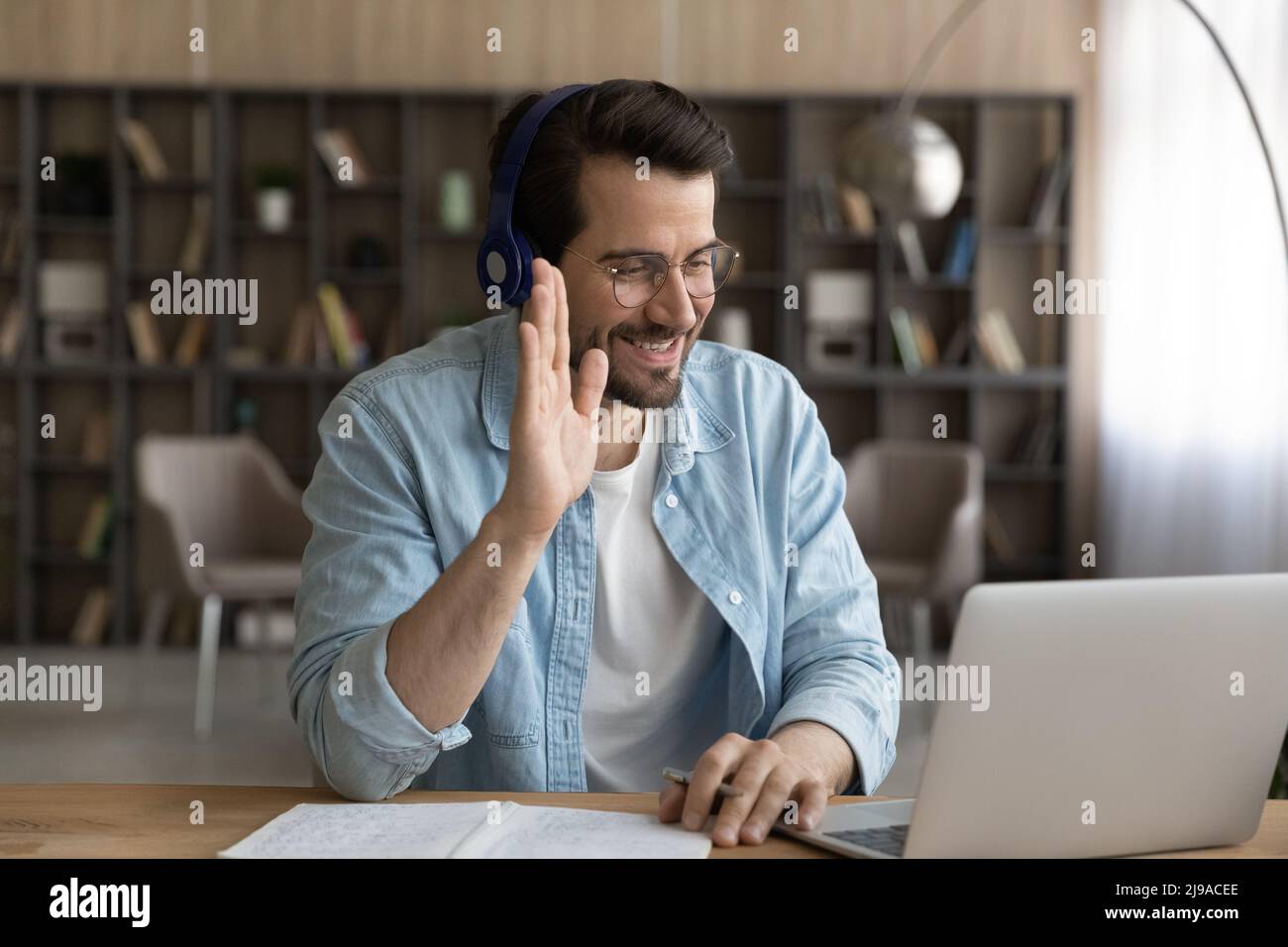 Millennial guy in headset wave hand meet tutor by pc Stock Photo - Alamy