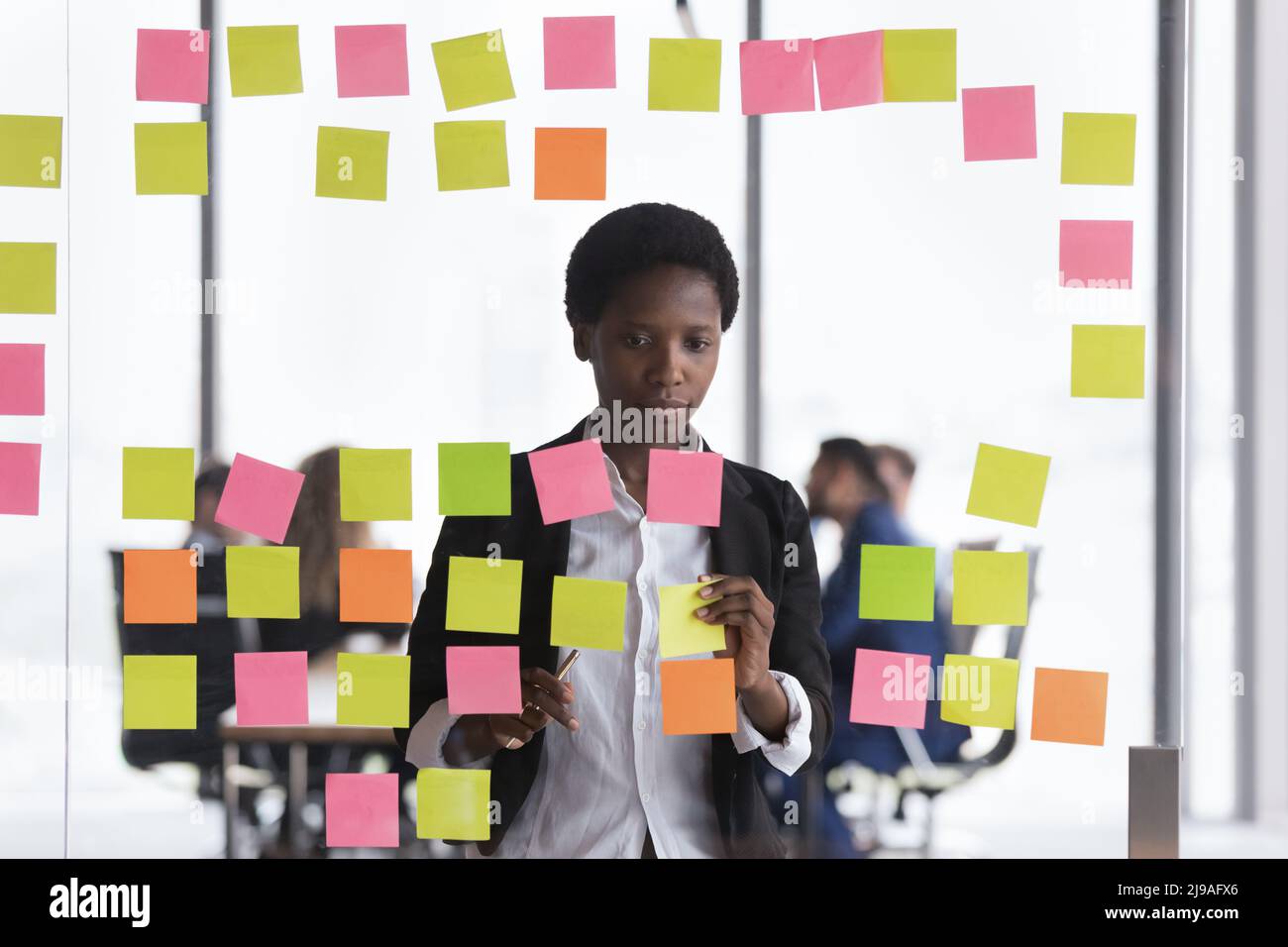 African woman attaching sticky notes on transparent wall in boardroom ...