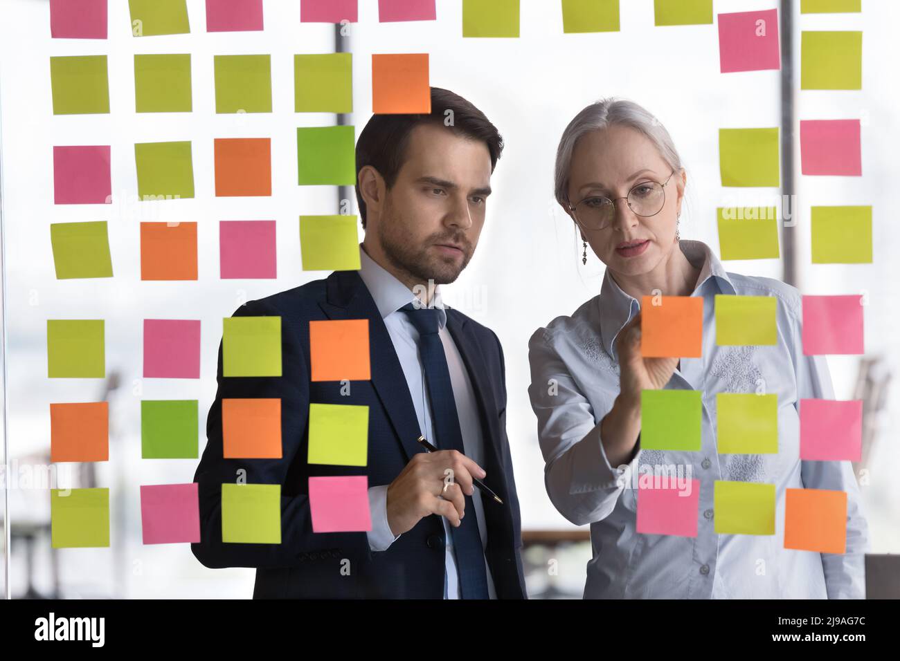 Office employees writing on sticky notes attached on wall Stock Photo ...