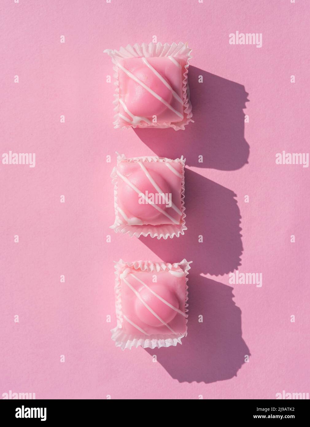 Pink fondant icing on sponge cakes set on a pastel pink background ...