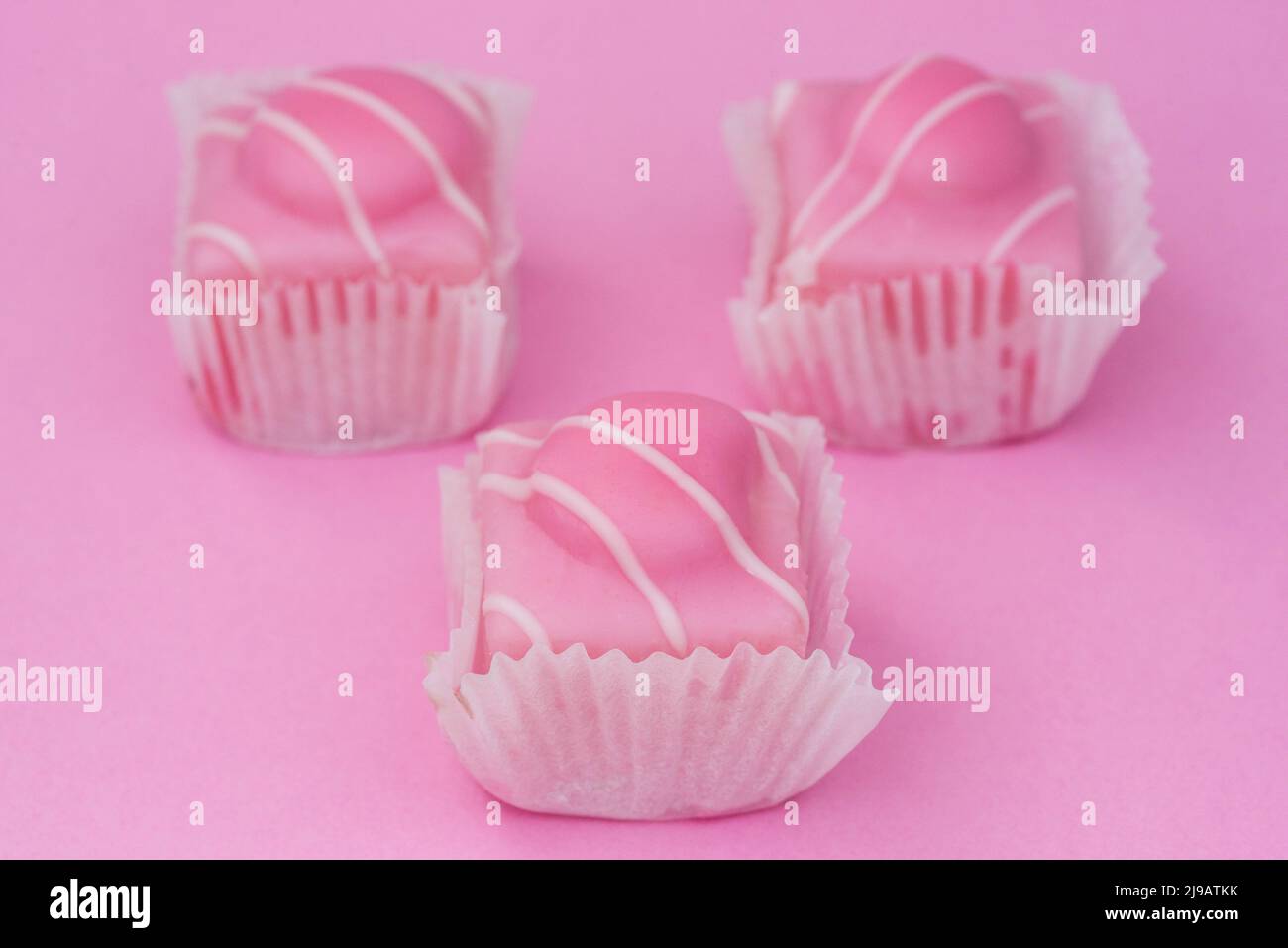 Close up of pink fondant icing on sponge cakes set on a pastel pink ...