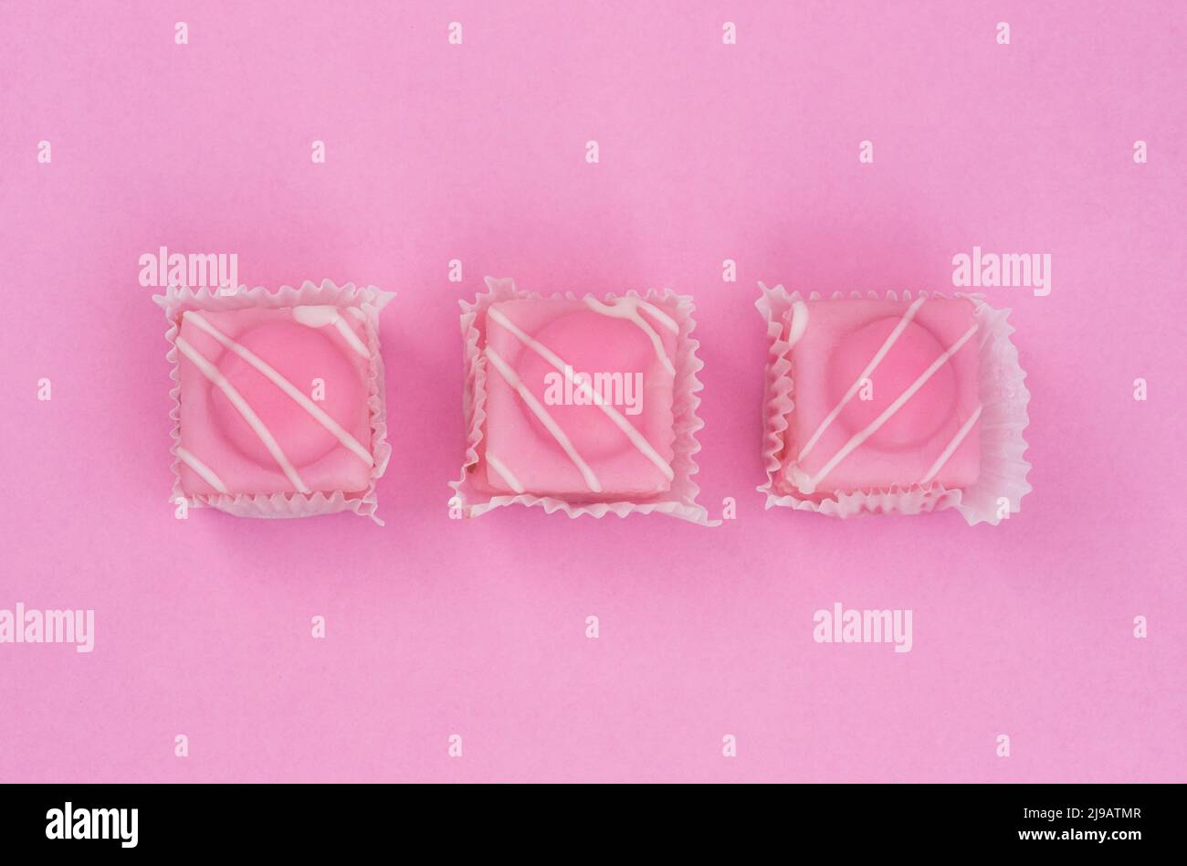 Pink fondant icing on sponge cakes set on a pastel pink background ...