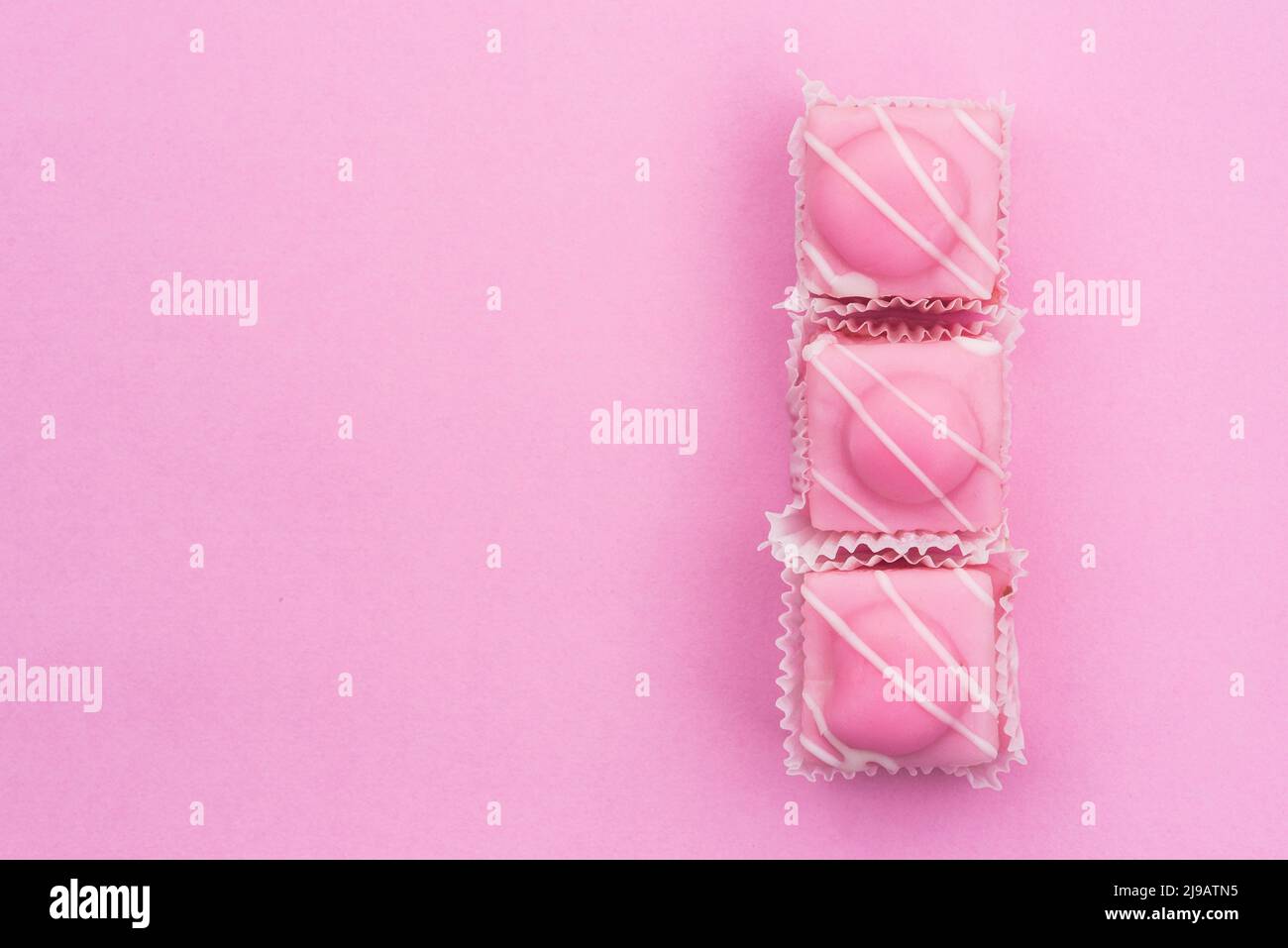 Pink fondant icing on sponge cakes set on a pastel pink background ...