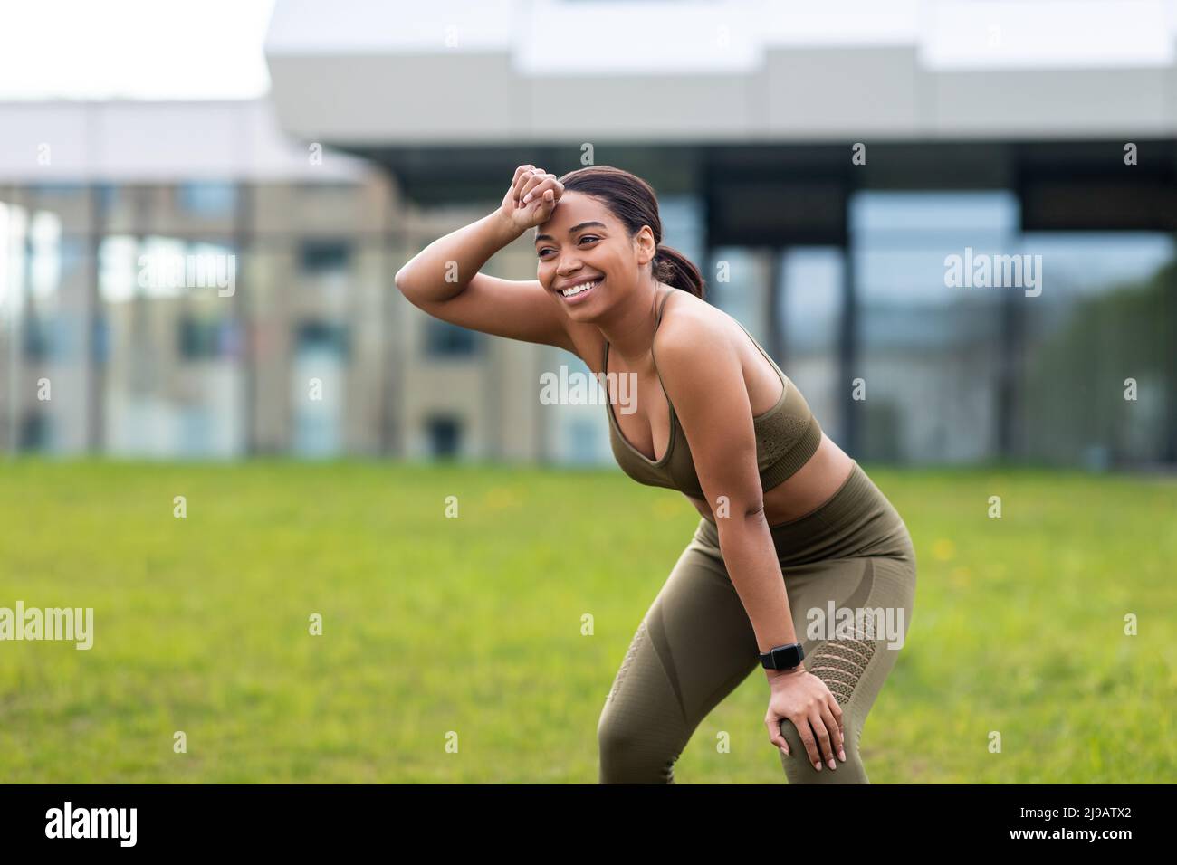 Happy tired young black woman wiping sweat from forehead after jogging ...