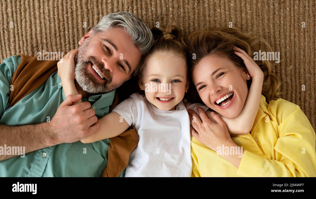 Joyful Parents And Daughter Embracing Lying On Floor At Home Stock ...
