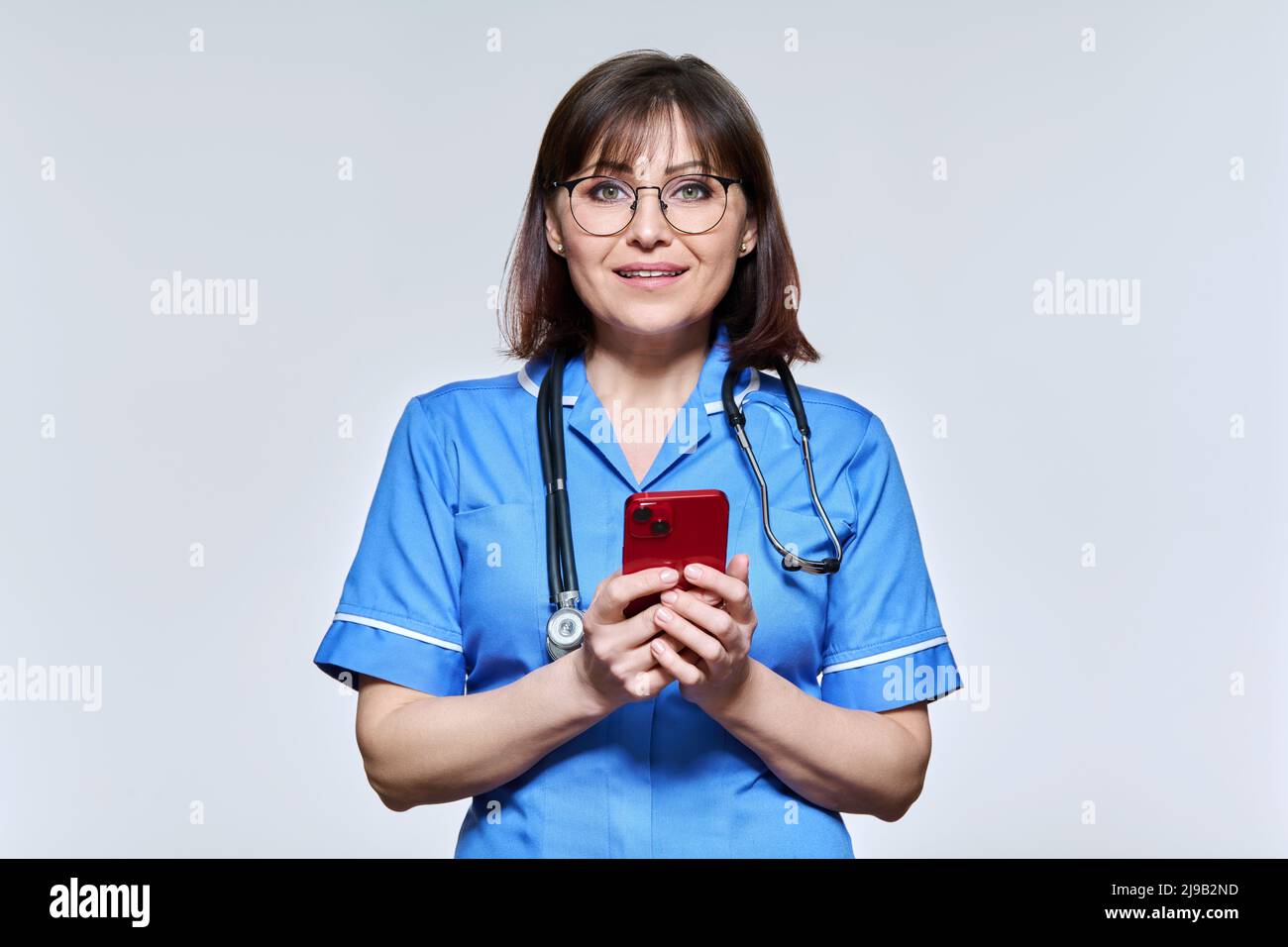 Portrait of female nurse with smartphone in hands, looking at camera on ...