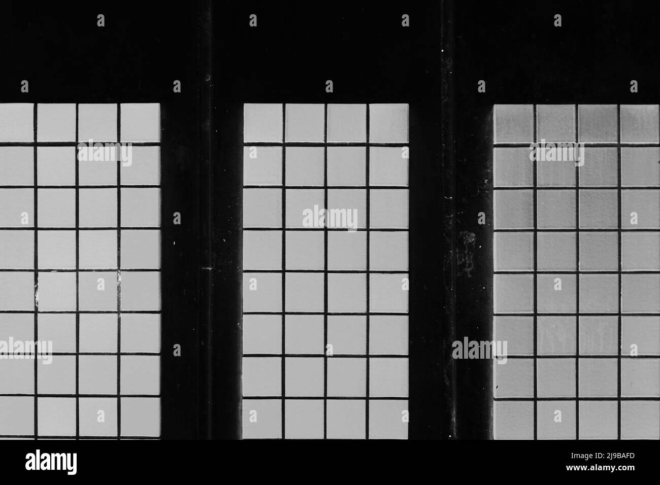 Square tiles on a wall in a grid repeat pattern in black and white film ...