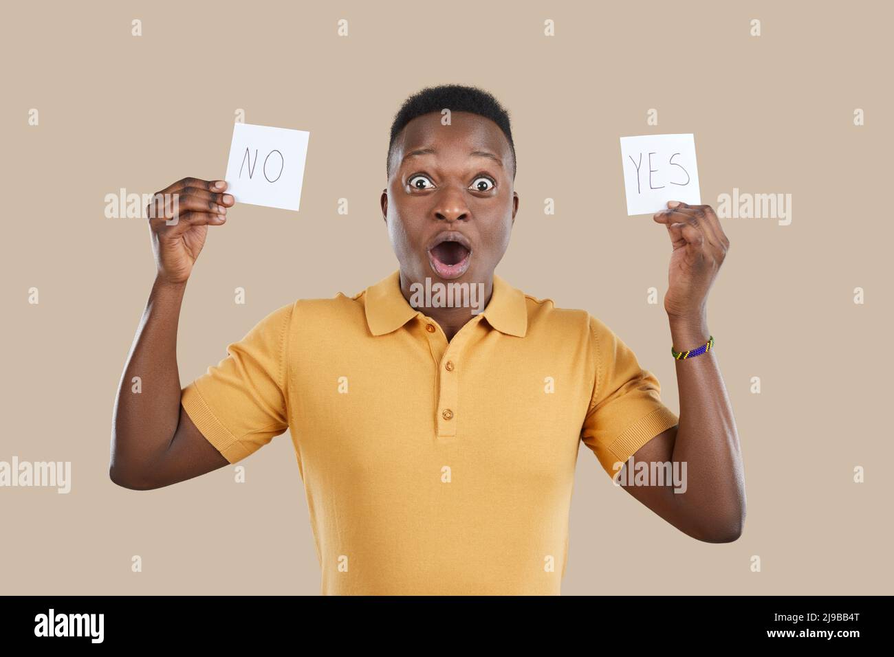 Funny confused young man holding YES and NO sticky notes and trying to ...