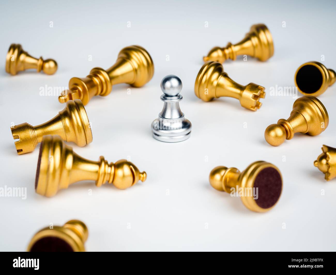 A silver pawn chess piece standing alone in the middle of many fallen ...