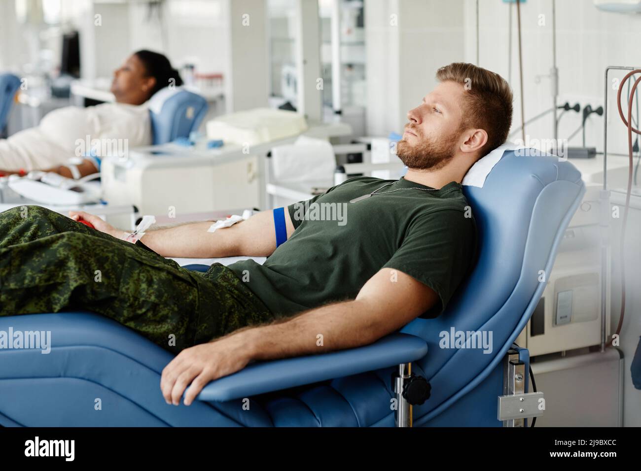 Side view portrait of military man donating blood while laying in chair ...