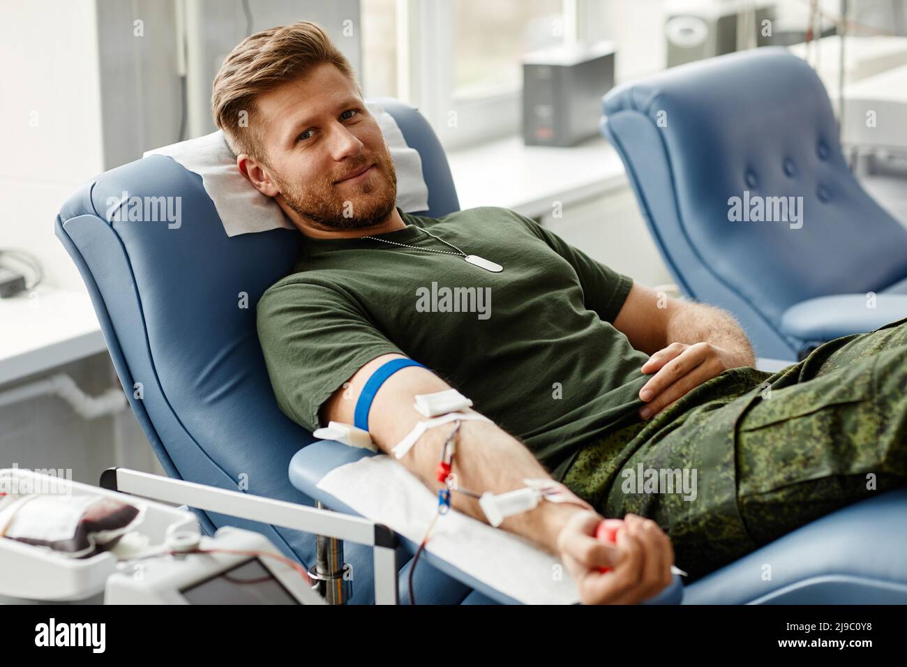 Portrait of smiling young man giving blood at donor center in comfort ...