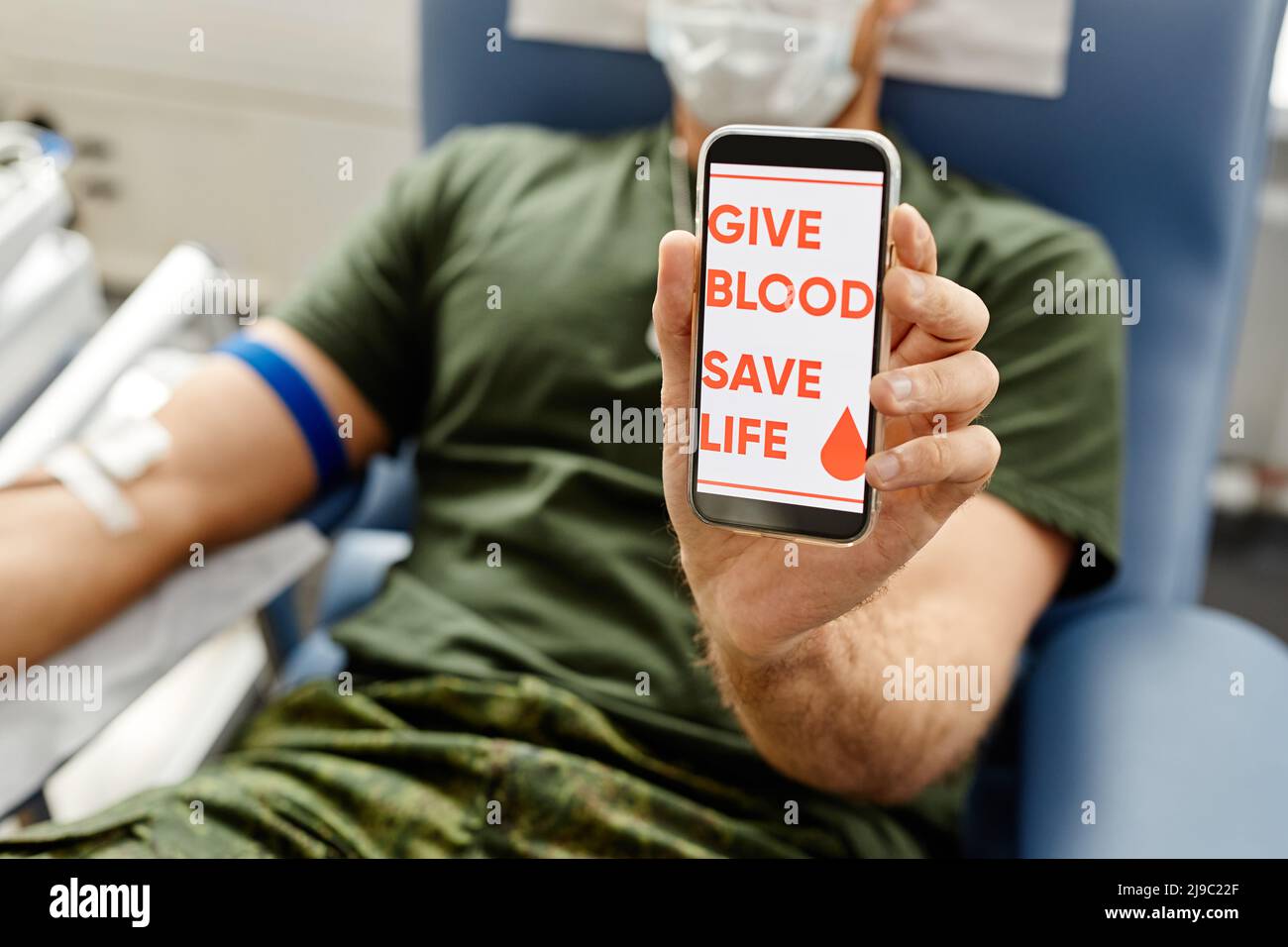 Closeup of soldier donating blood and holding smartphone to camera with ...