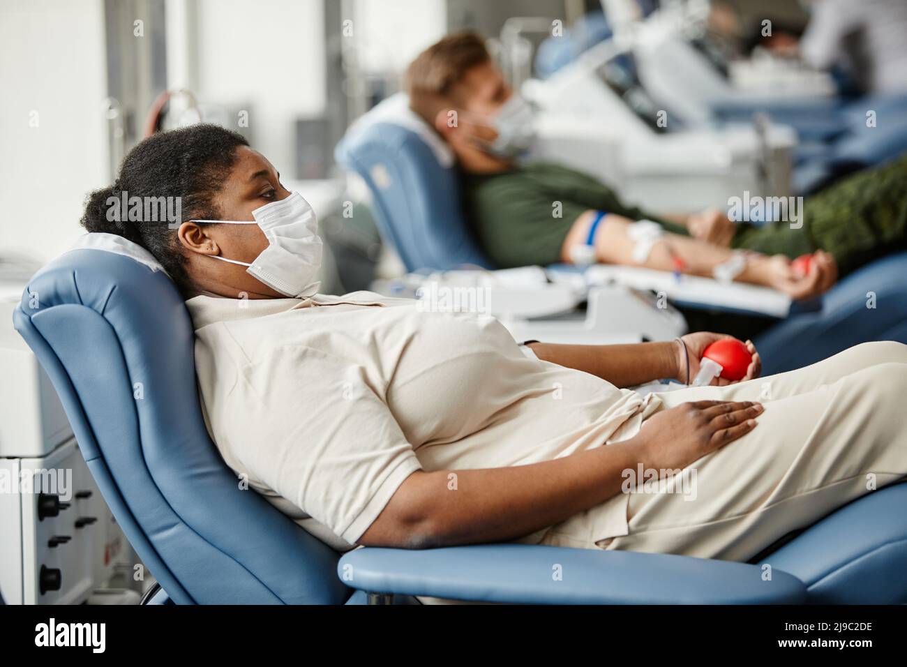 Side view portrait of people wearing masks while giving blood in row at ...