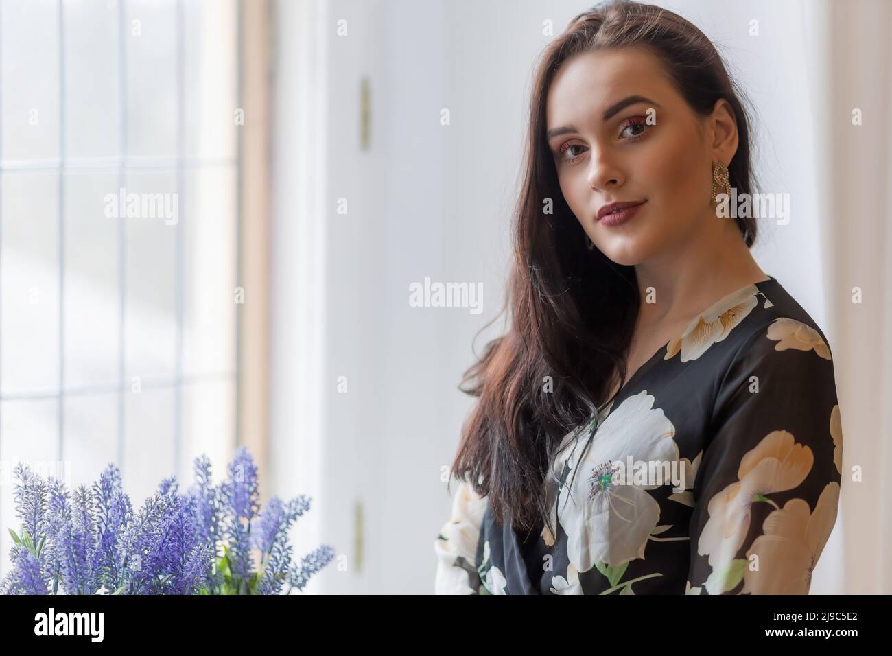Attractive Dark Haired Girl Is Posing Next To Purple Flowers In Windows