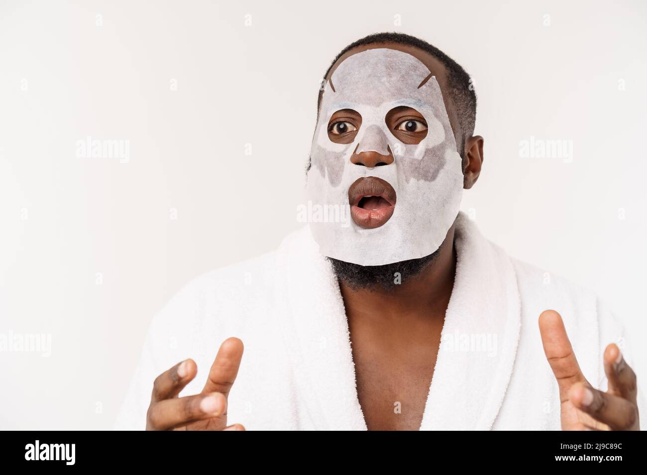A young man with paper mask on face looking shocked with an open mouth ...