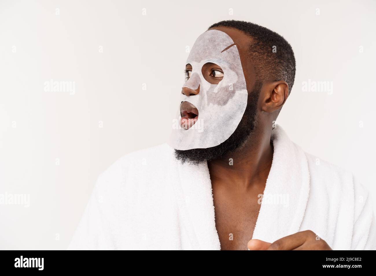 A young man with paper mask on face looking shocked with an open mouth ...