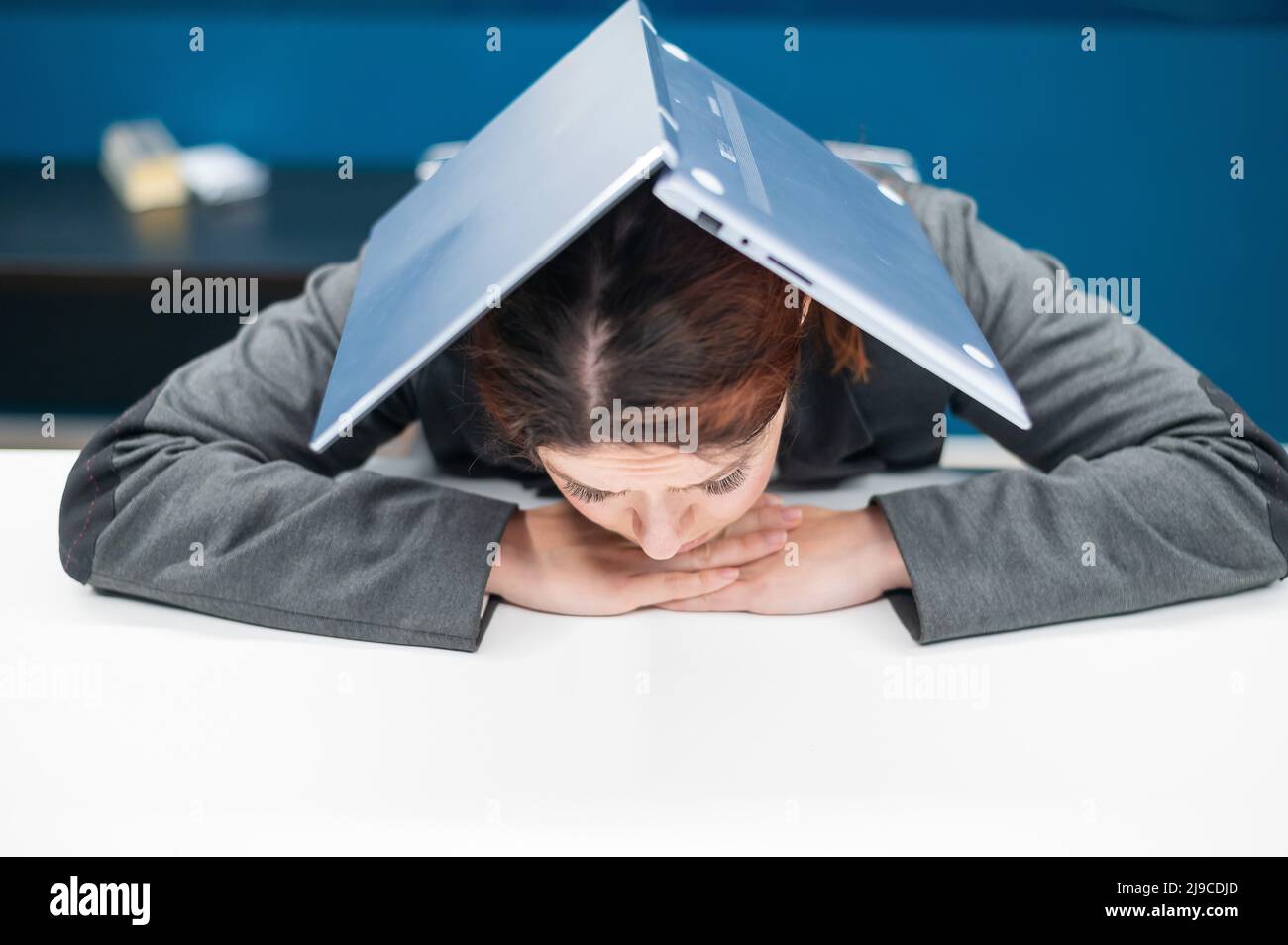Problems at work. An exhausted woman folded her laptop over her head at ...