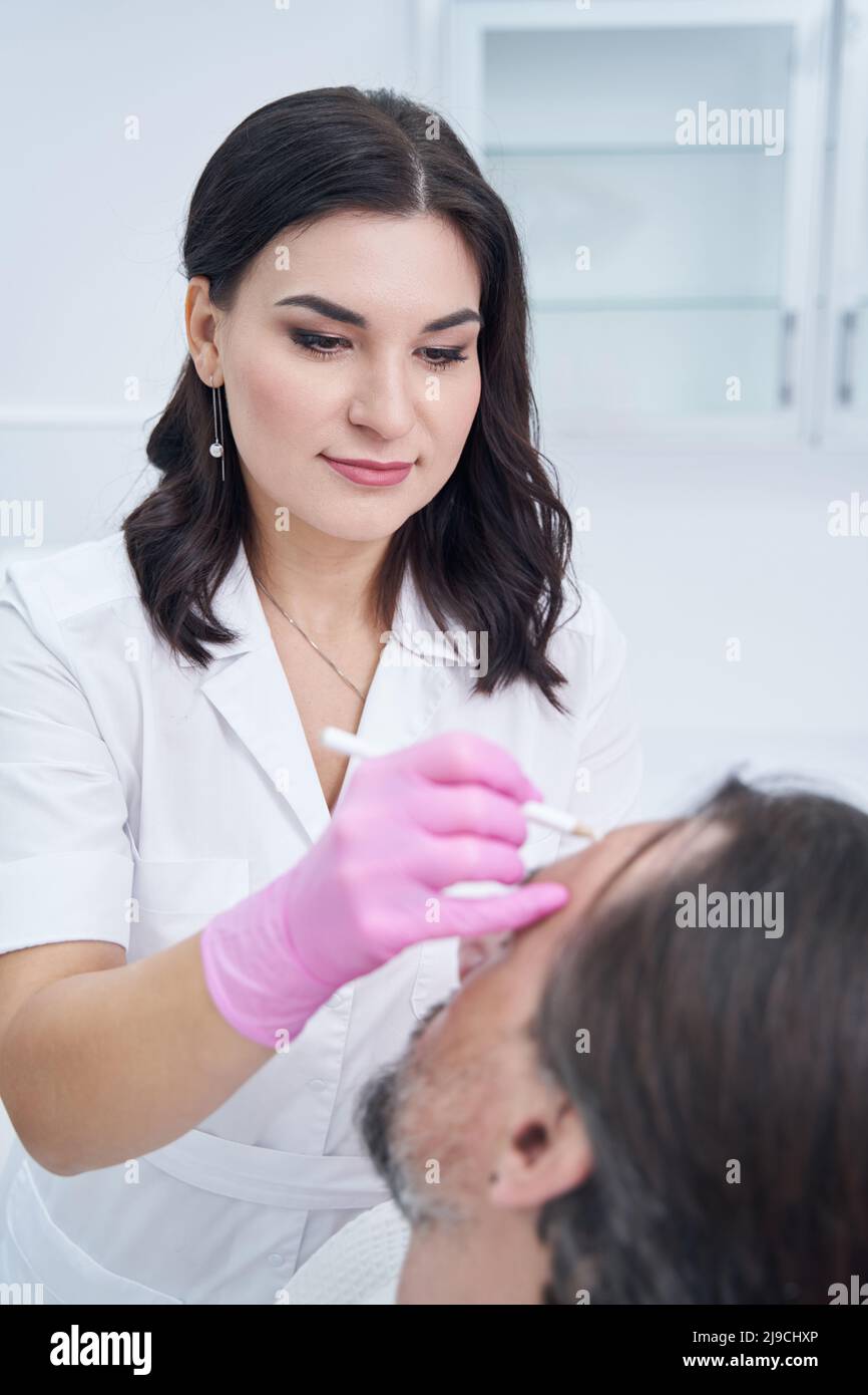 Cosmetologist making marks on adult male face before injection ...