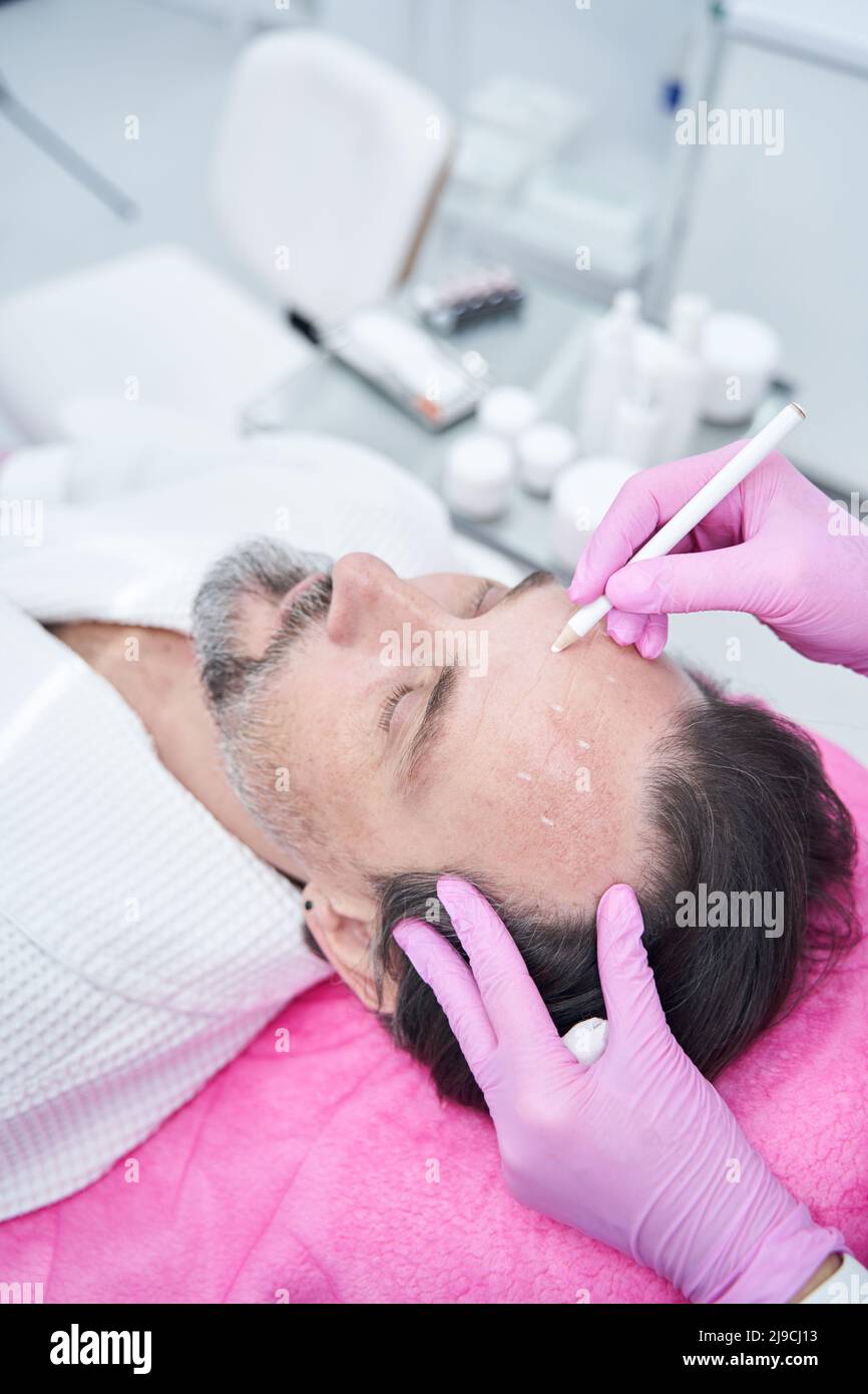 Lady cosmetologist marking marks an adult patient forehead before ...