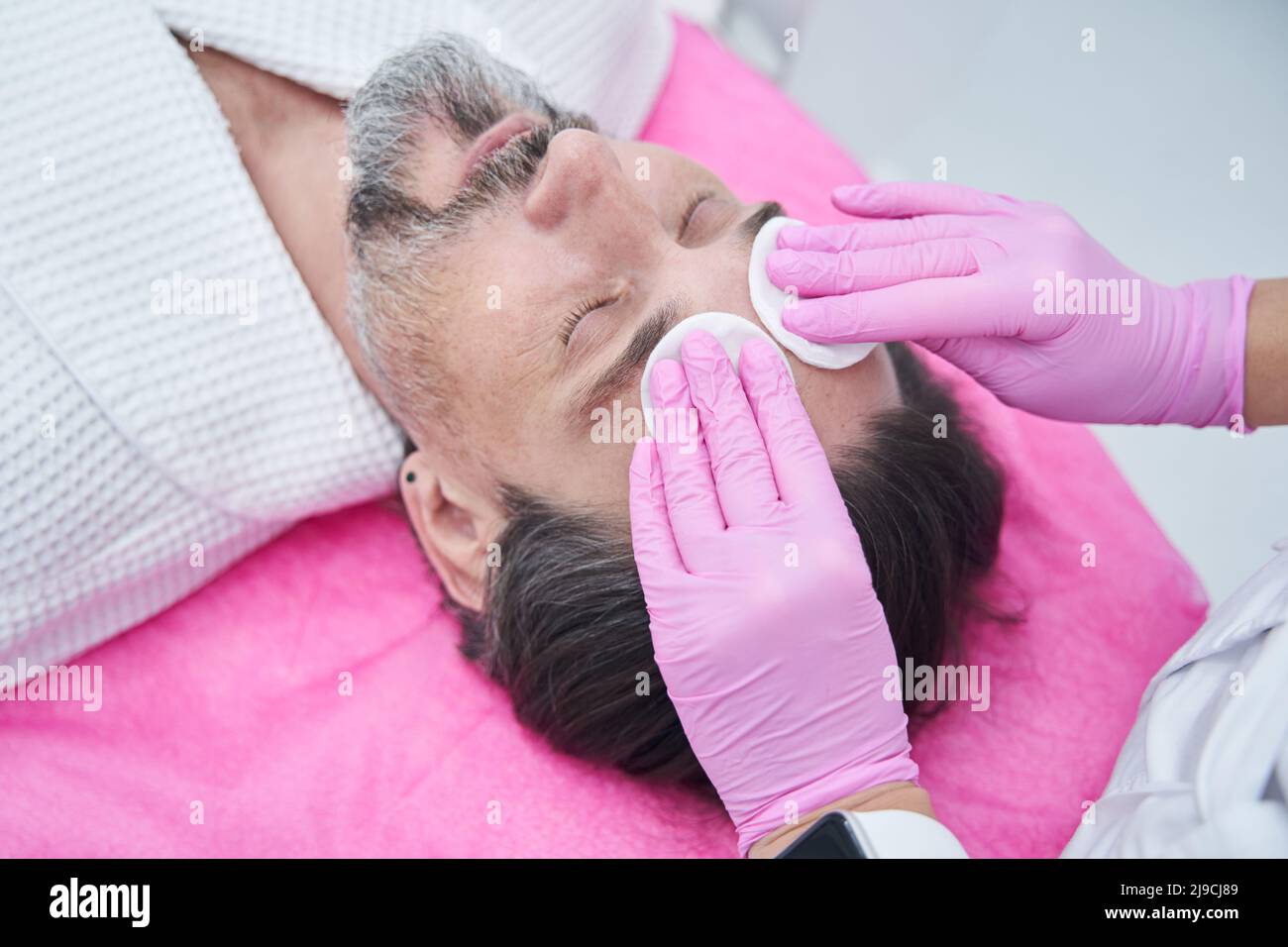 Female cosmetologist wiping adult patient face before cosmetic ...