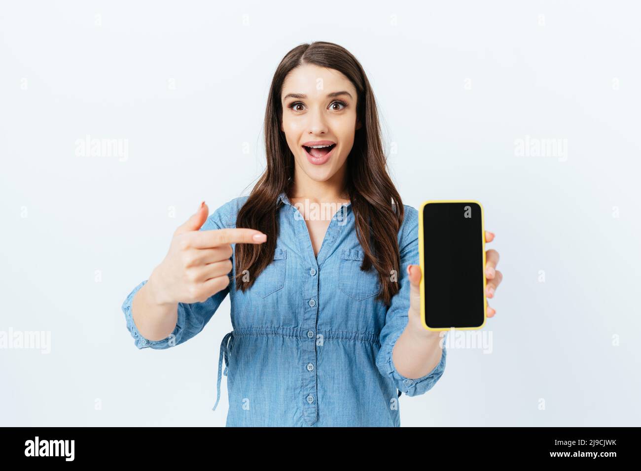 Cheerful young woman showing smartphone with blank screen pointing her ...
