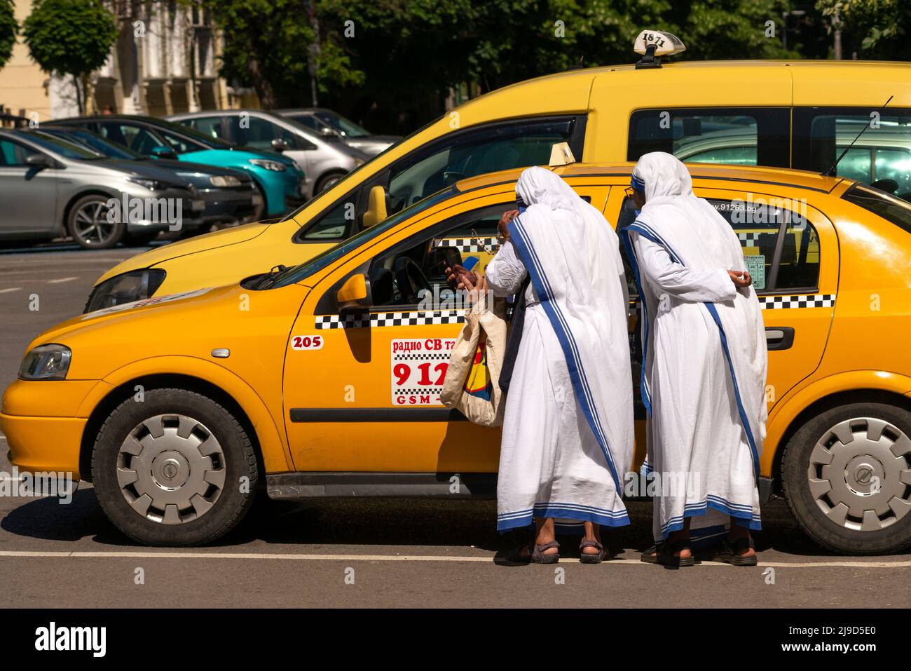 African nuns in white robes asking for fare at yellow taxi cab in Sofia ...