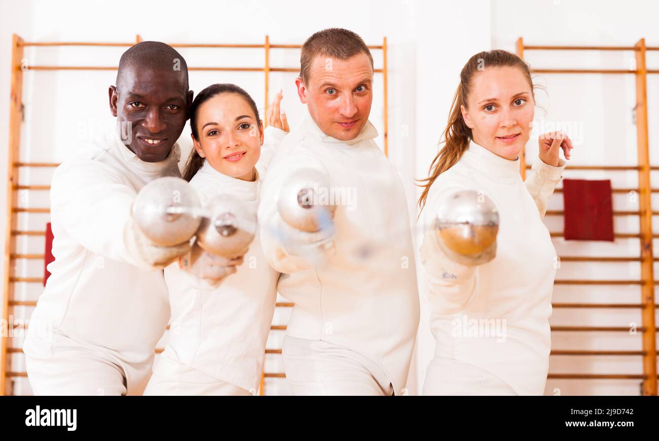 Group of smiling fencers posing with foils together at fencing room ...