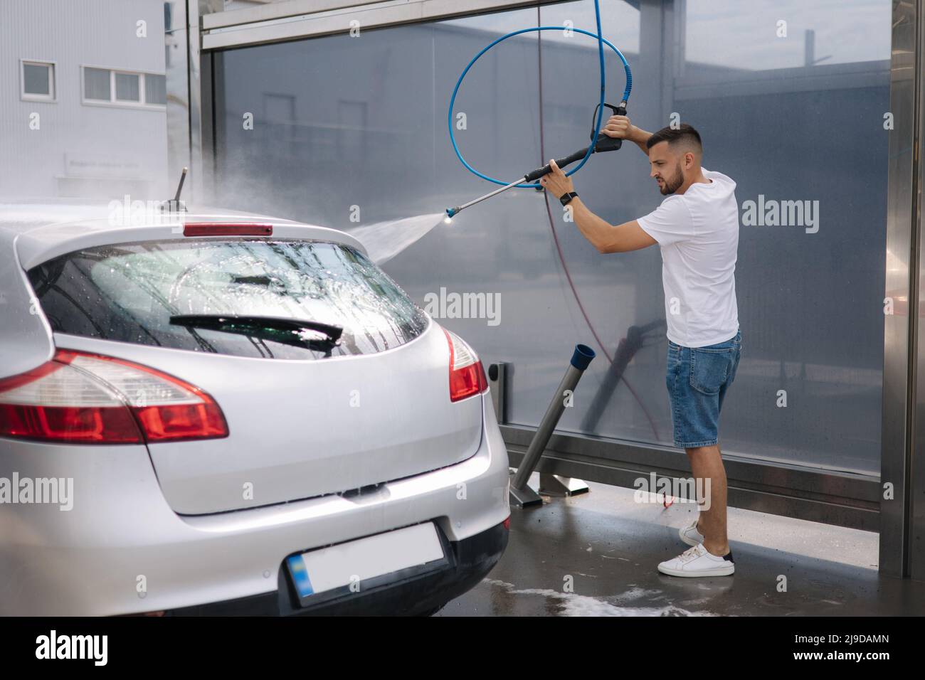 Back view of young man cleaning his car with a jet sprayer. Self ...