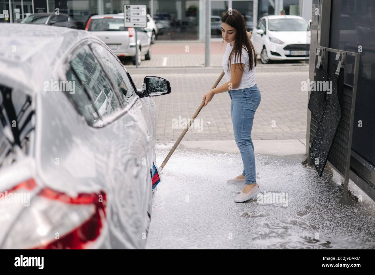 Attractive young woman washing her car with shampoo and brushes. Female ...