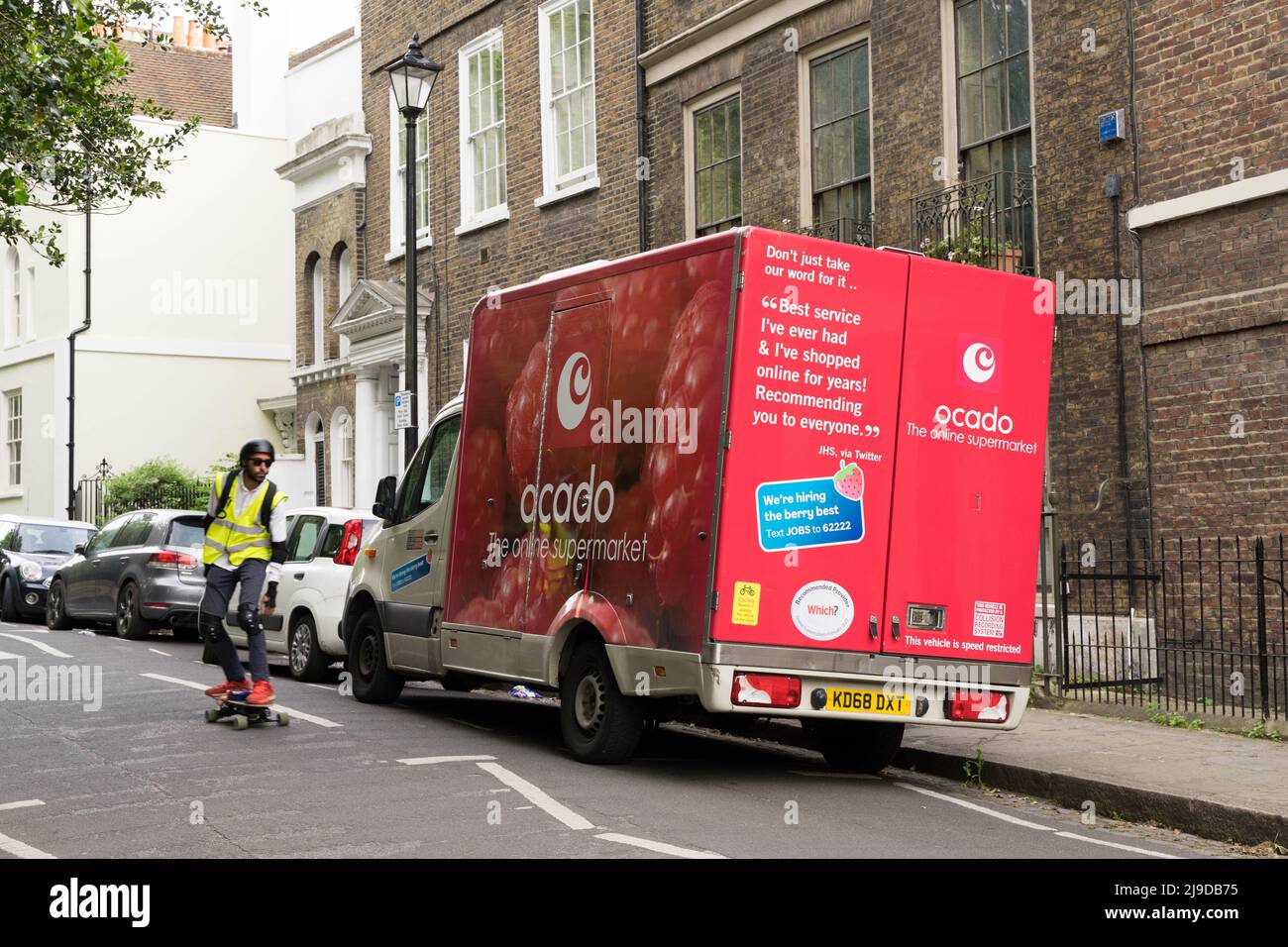 Ocado delivery van and skateboarder in high-viz skating past Greenwich ...