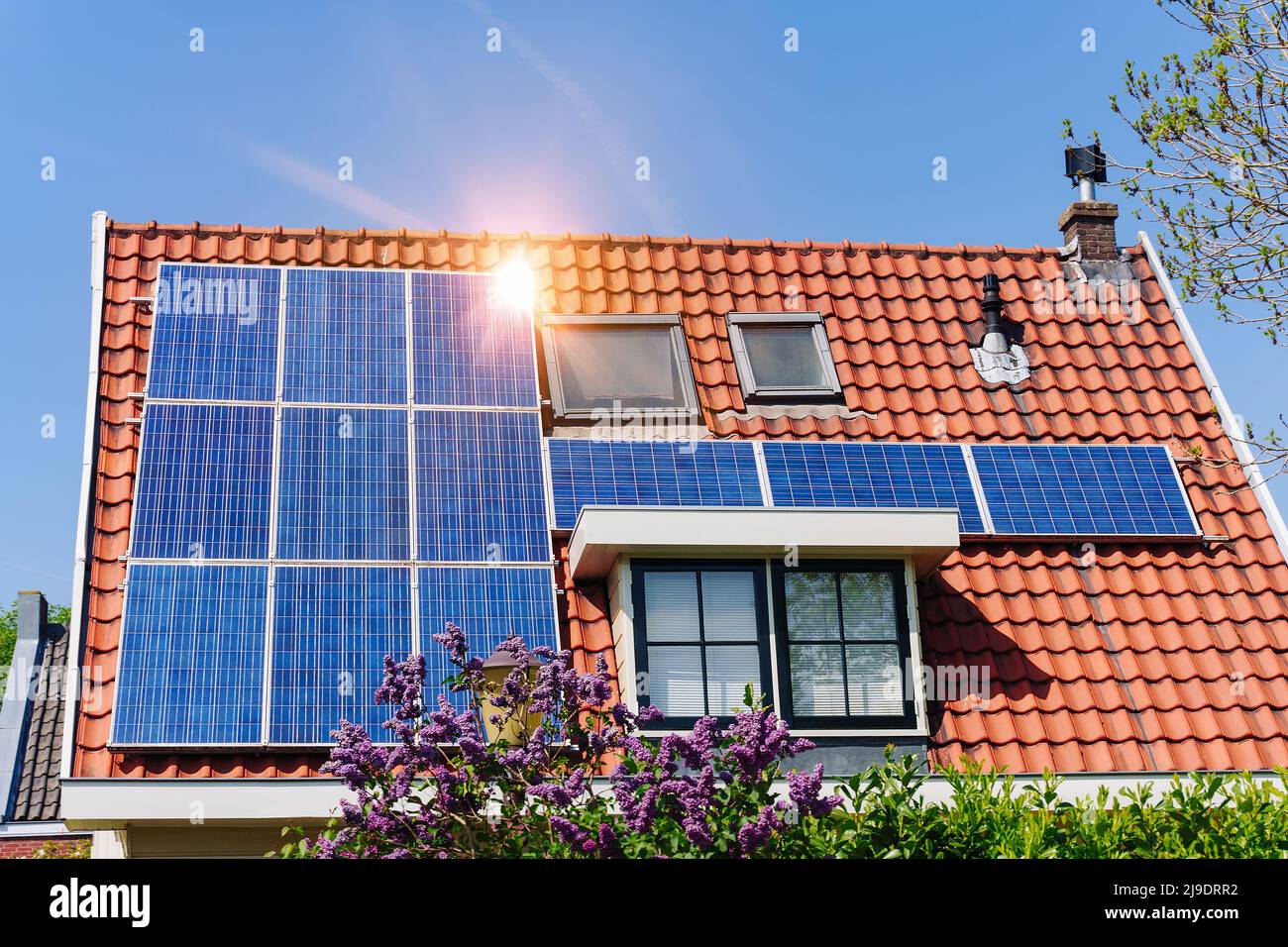 Solar panel on a red roof reflecting the sun and the cloudless blue sky ...