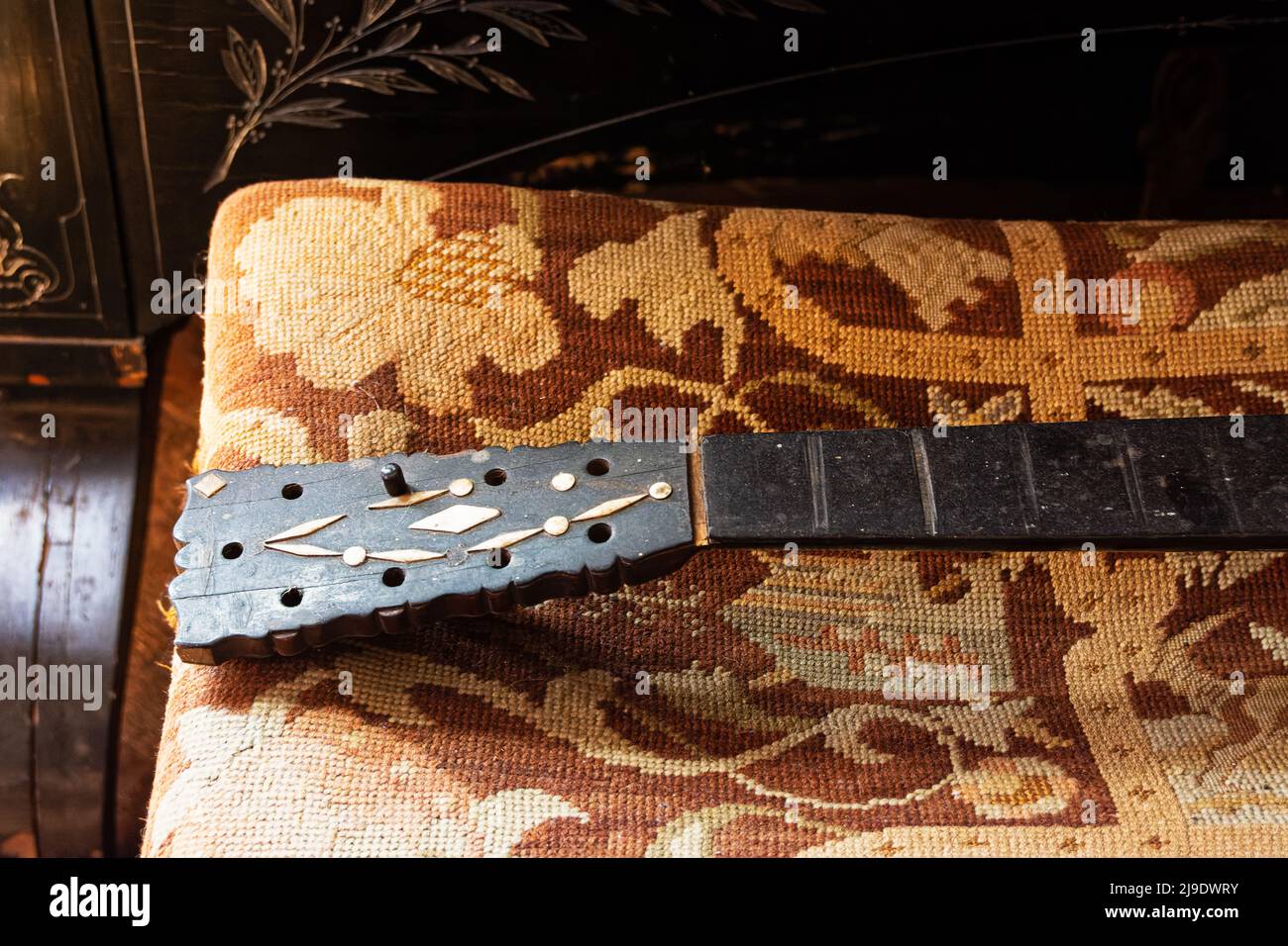 The neck of a vintage stringed instrument lays on a cloth covered chair ...