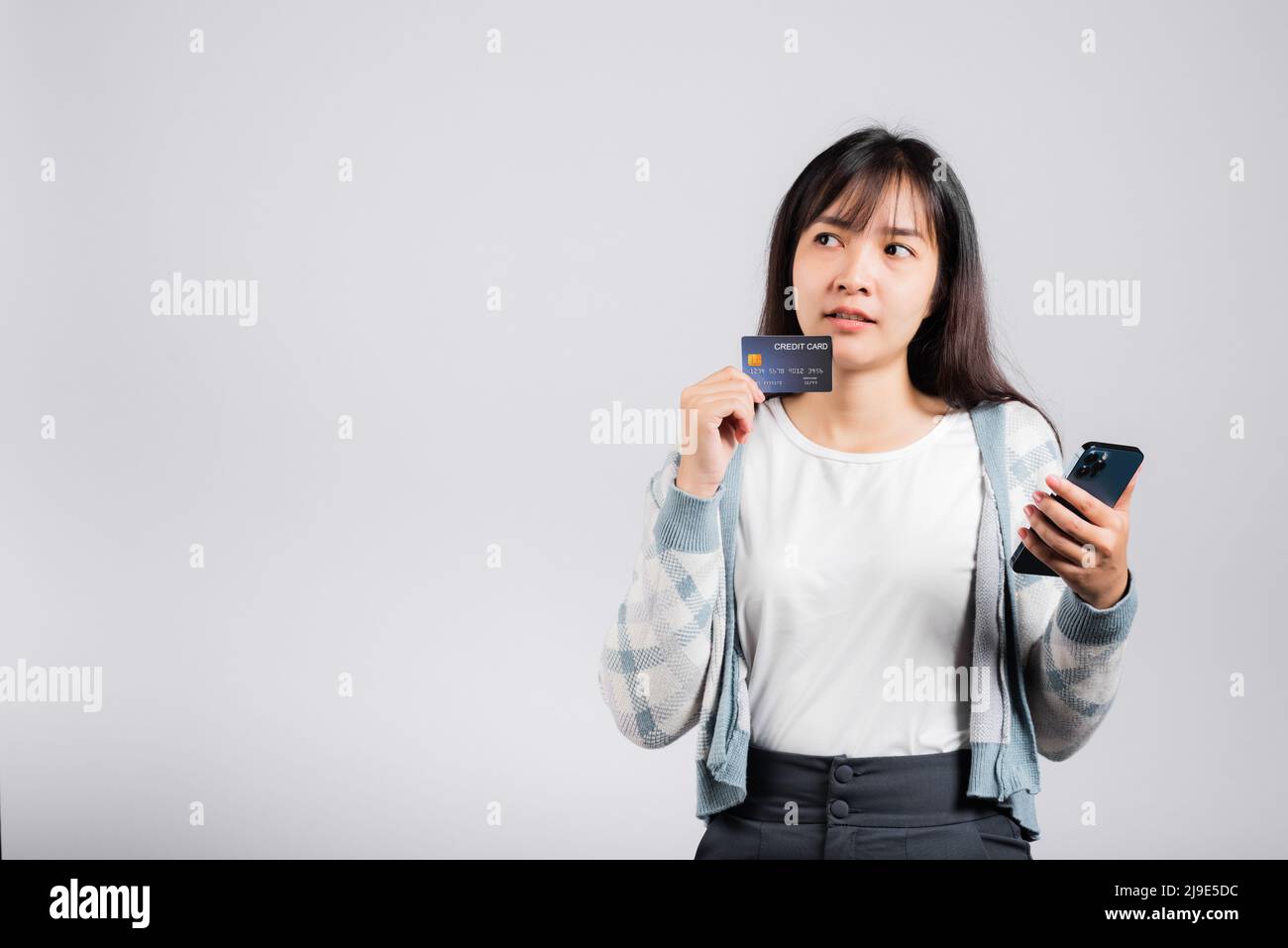 Woman excited smiling hold mobile phone and plastic debit credit bank card for payment studio ...