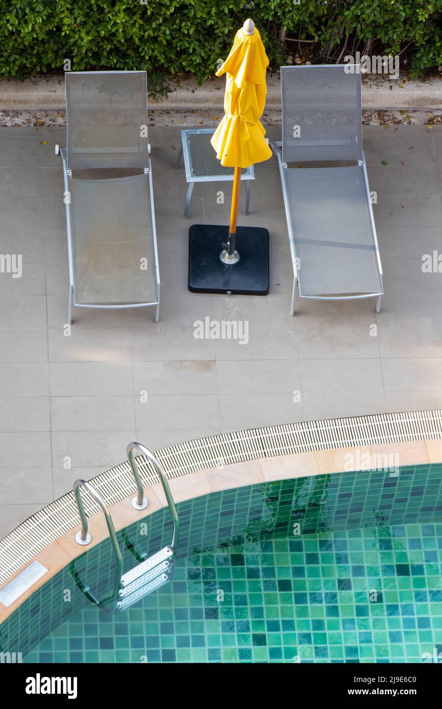 Empty deck chairs with closed parasol by the swimming pool at sunset ...