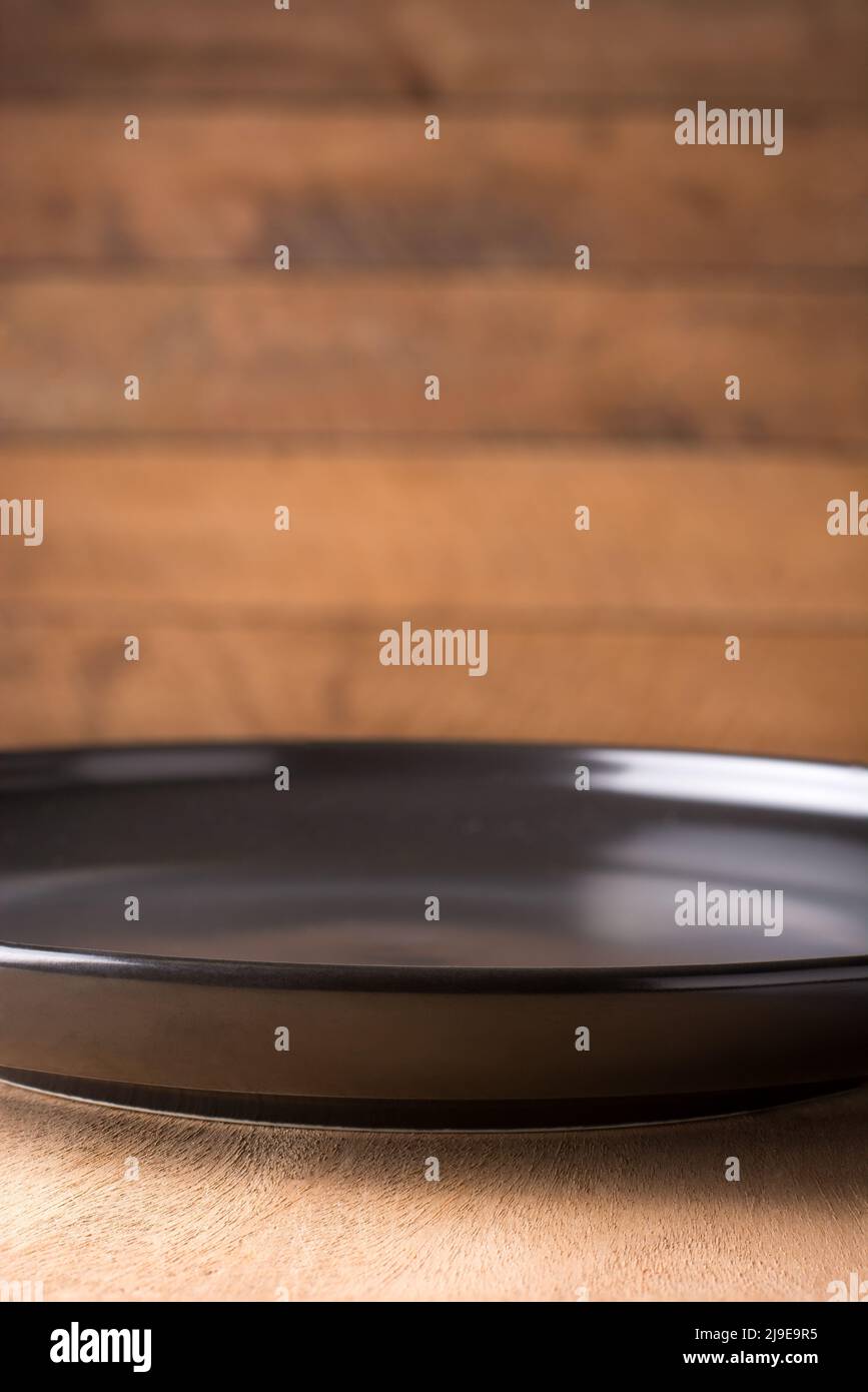 empty black plate on a wooden table top against blurry wooden ...