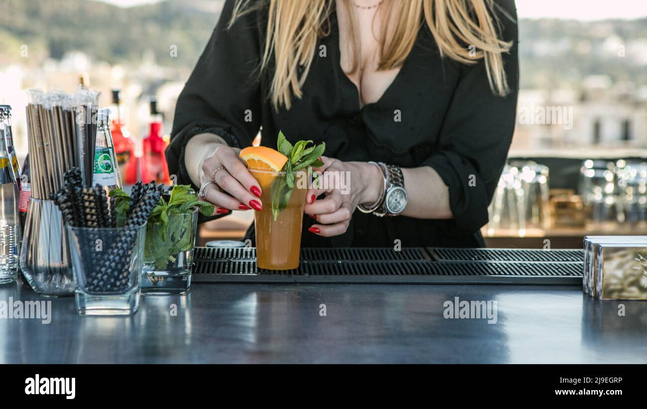 Expert barwoman is making cocktail at night club or bar. Orange juice ...