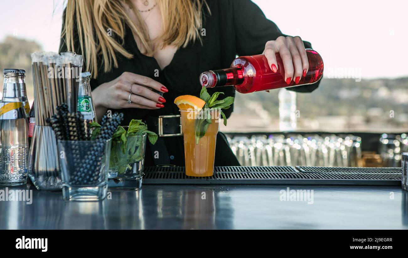 Expert barwoman is making cocktail at night club or bar. Orange juice ...