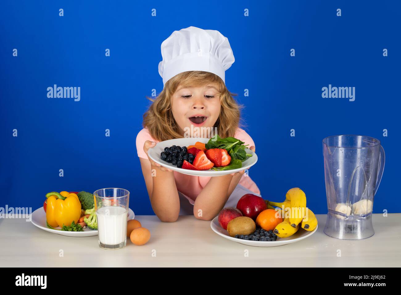Child wearing cooker uniform and chef hat hold plate with fruits ...