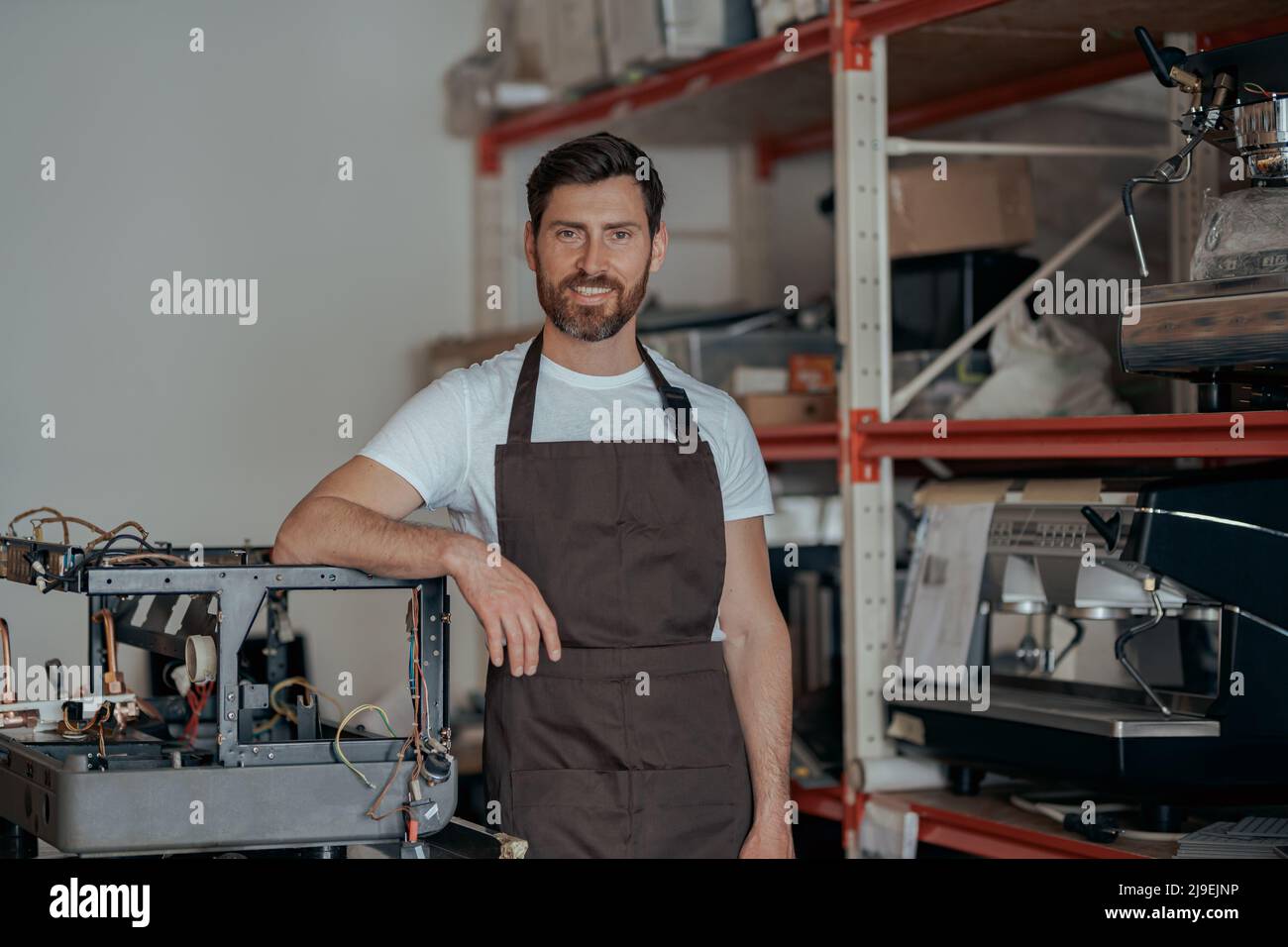 Portrait of repairman in uniform standing on workshop of coffee ...