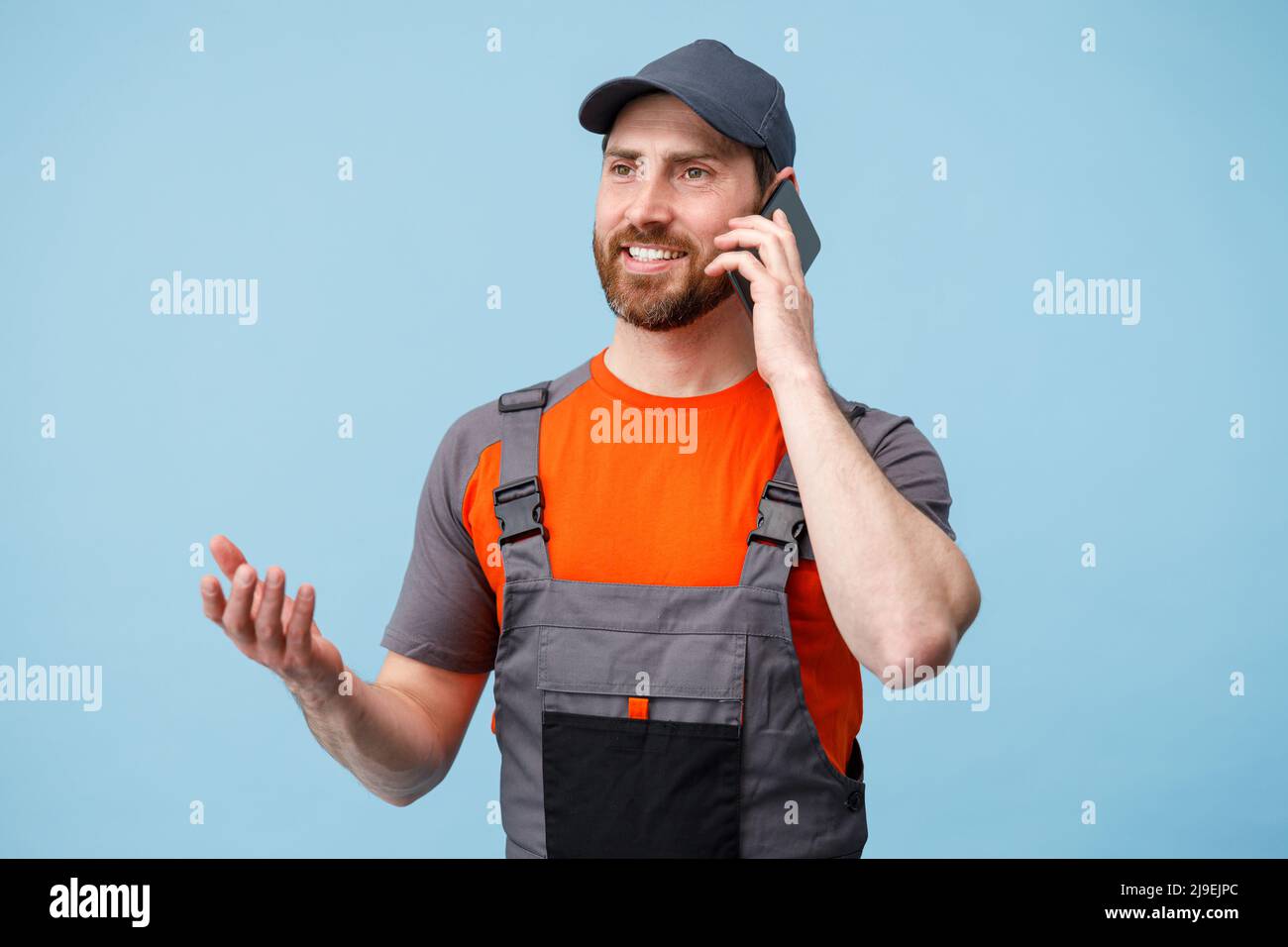 Delivery employee man in uniform talk on mobile phone on blue studio ...